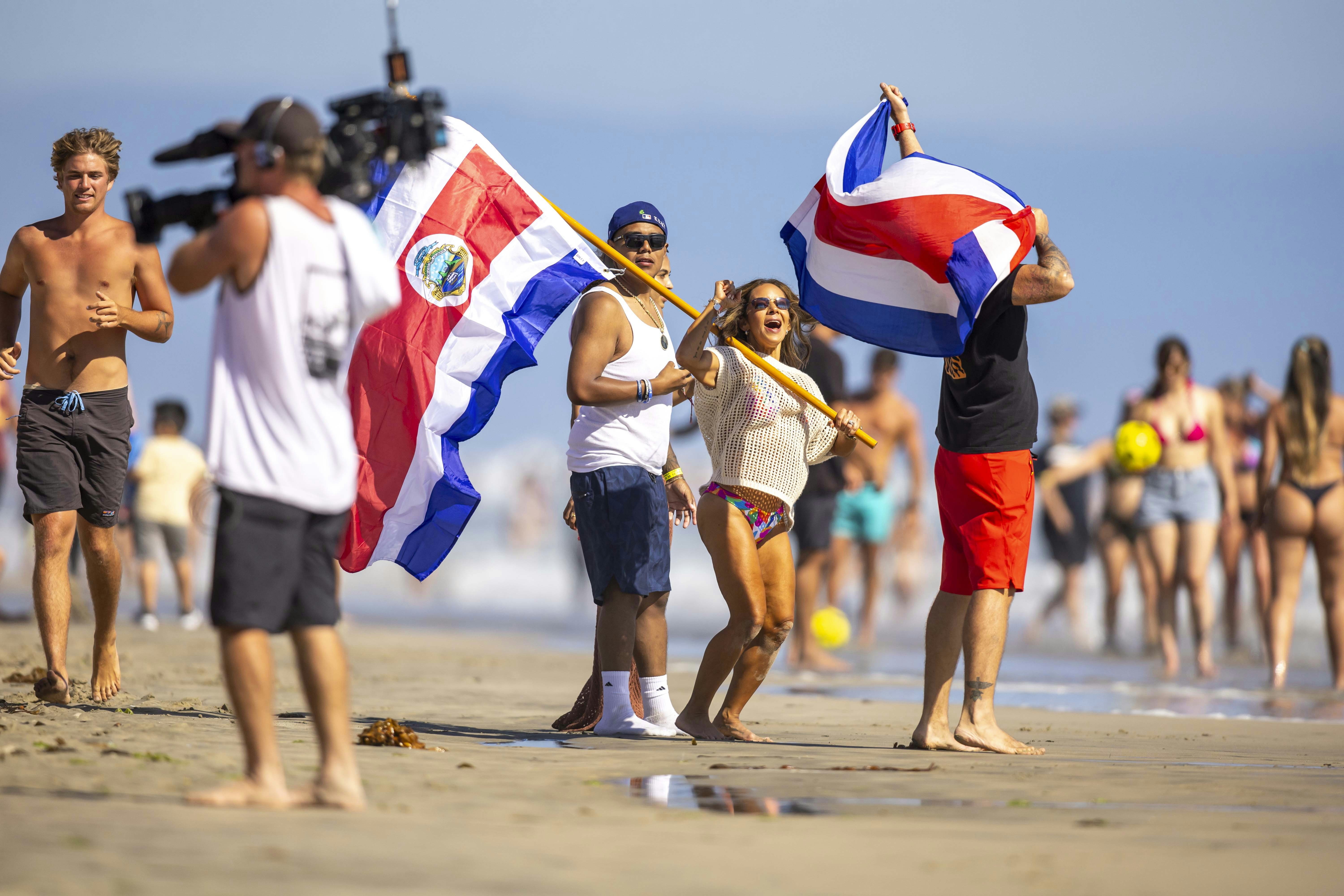 People wave costa rican flags on a sunny beach.
