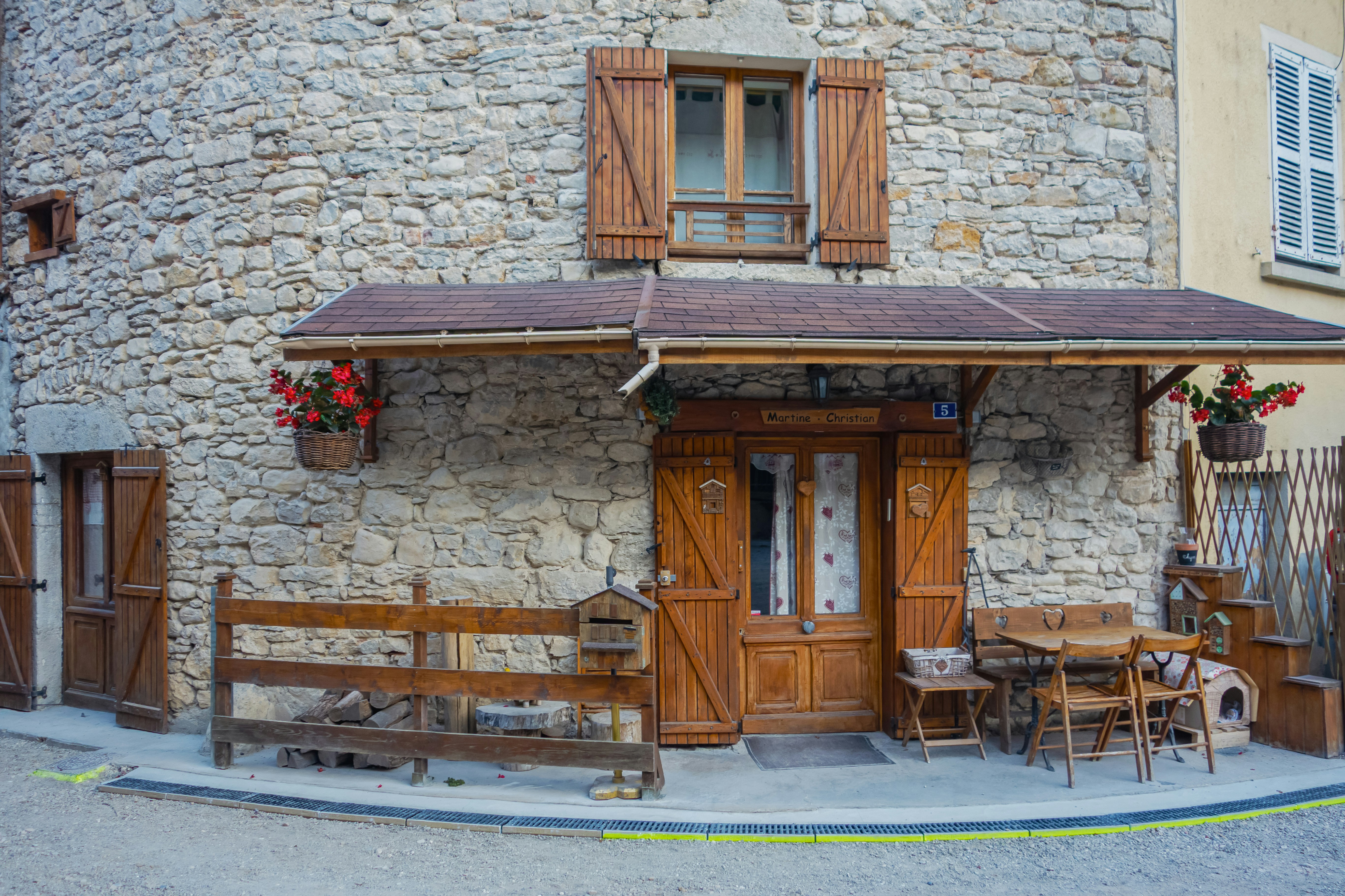 La rénovation de cette terrasse a redonné vie à ce coin suspendu de charme et d'authenticité, où le bois neuf embrasse la pierre ancienne dans une étreinte de mémoire et de renouveau. | Stone building with wooden shutters and door