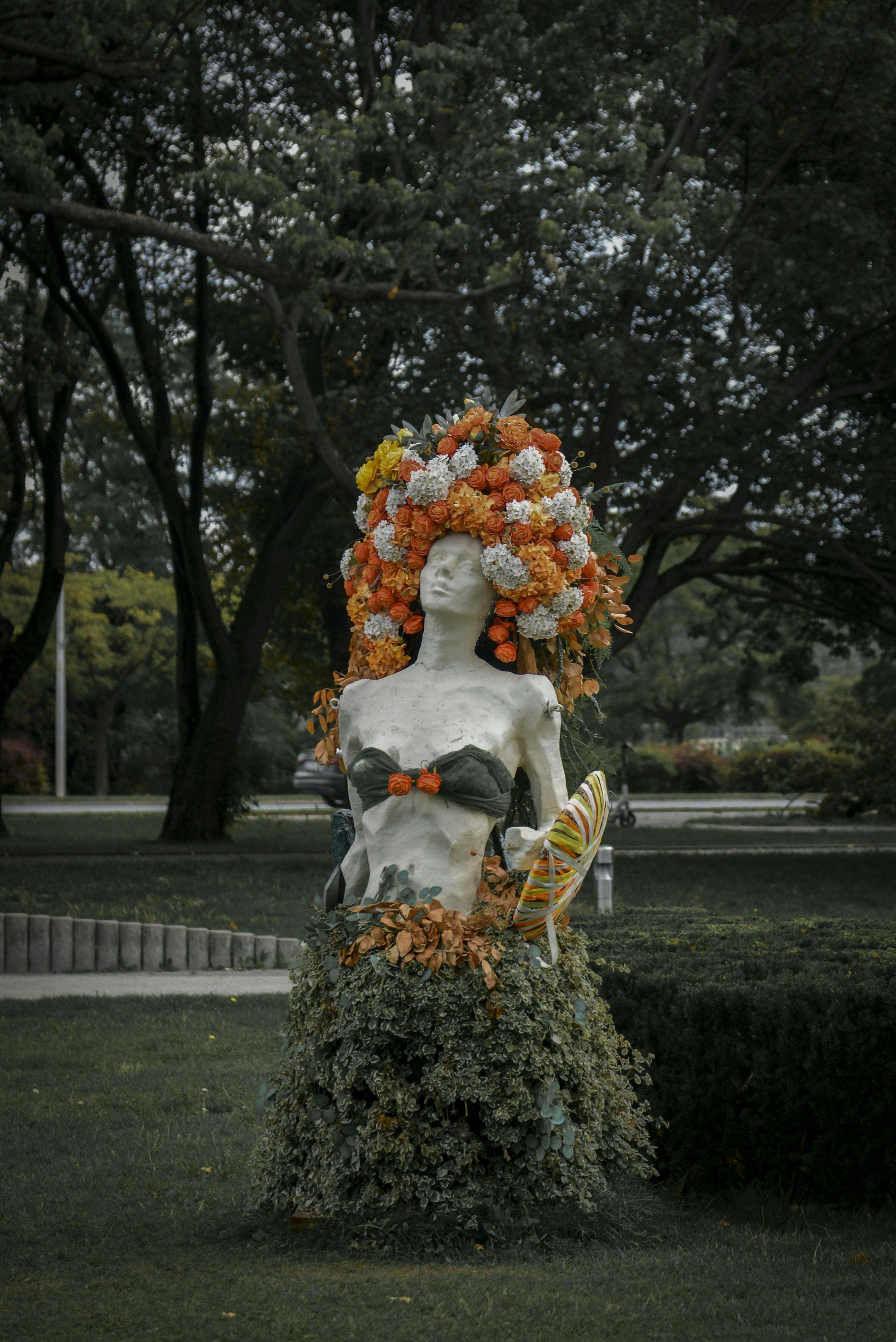 A statue adorned with vibrant flowers and greenery, embodying a fusion of art and nature in a serene park setting.