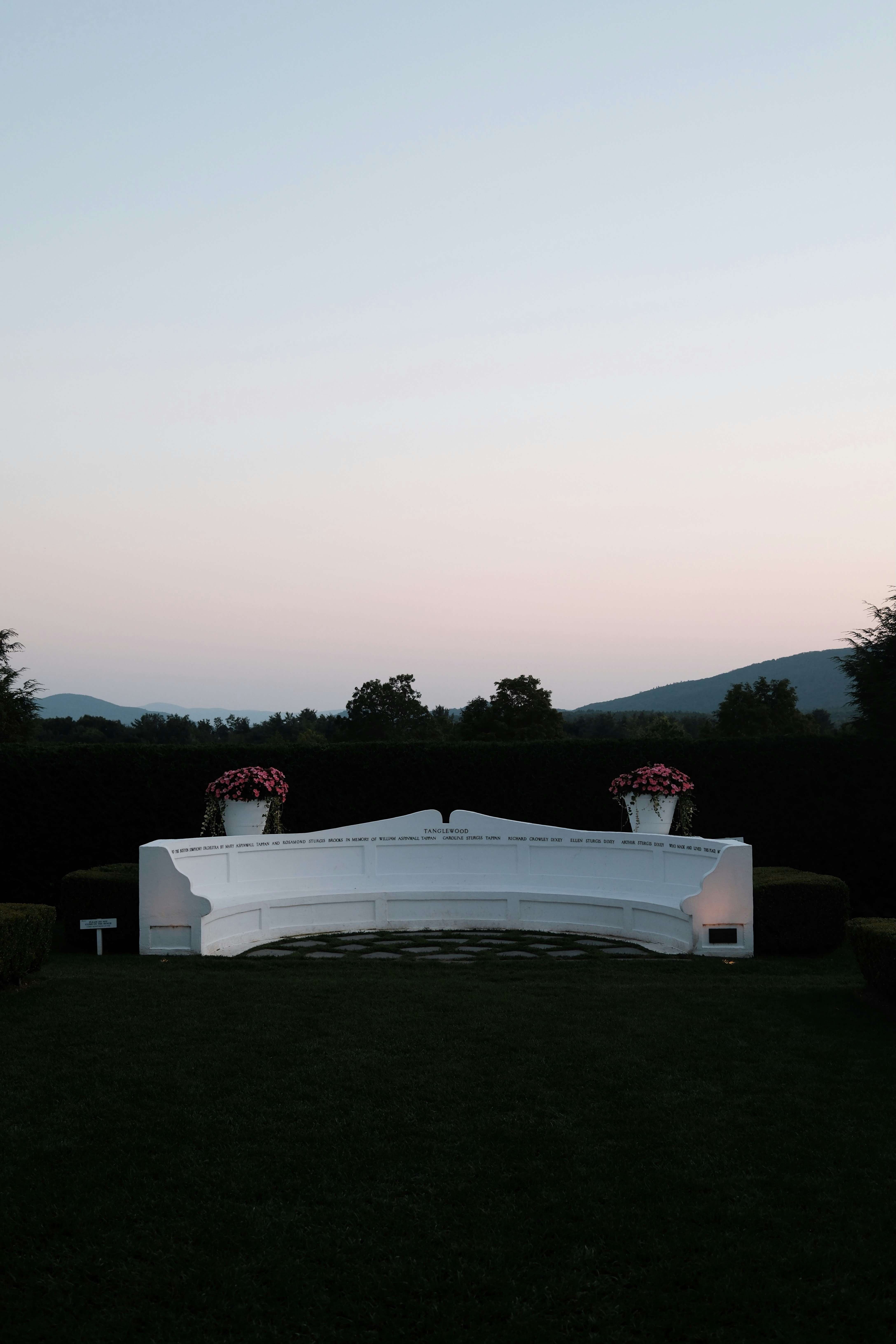White Crescent Bench at Dusk: Flowers, Hedge, and Distant Hills