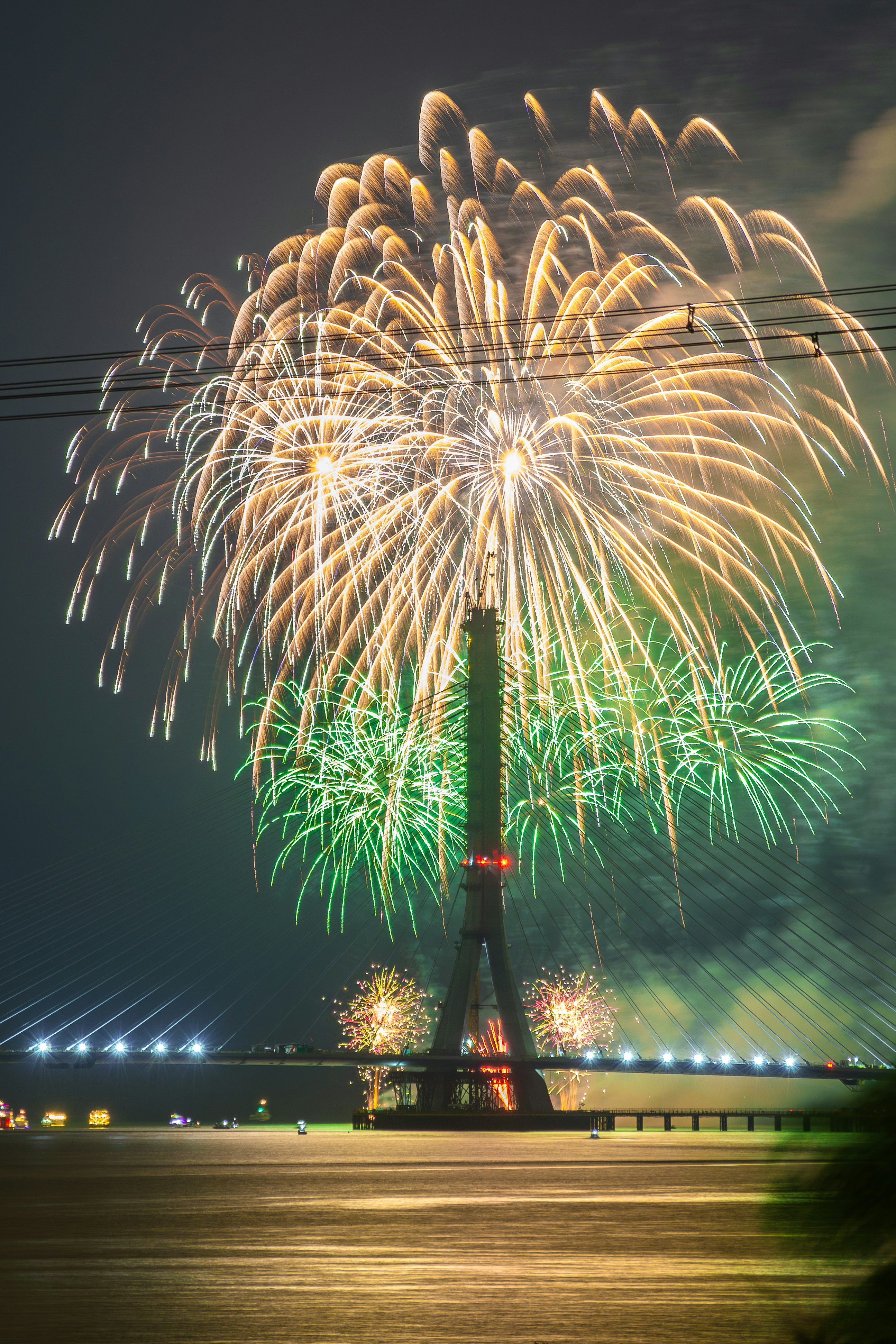 Colorful fireworks explode over a bridge at night