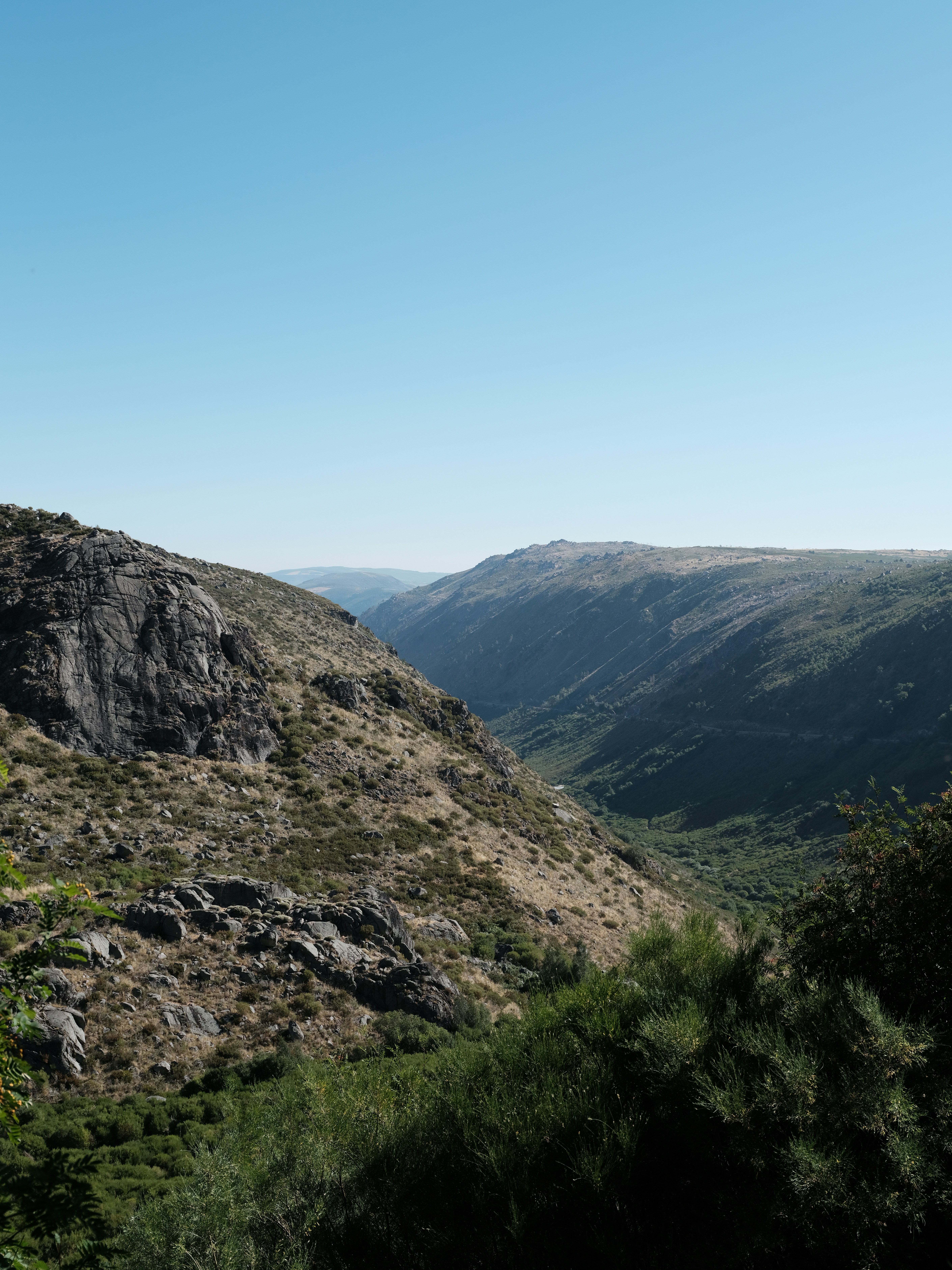 From above, the green path of the Zêzere Glacial Valley seems to guide the eye towards a distance we cannot yet see, reminding us that every journey begins with a horizon we do not fully understand. | Rocky mountain valley under a clear blue sky