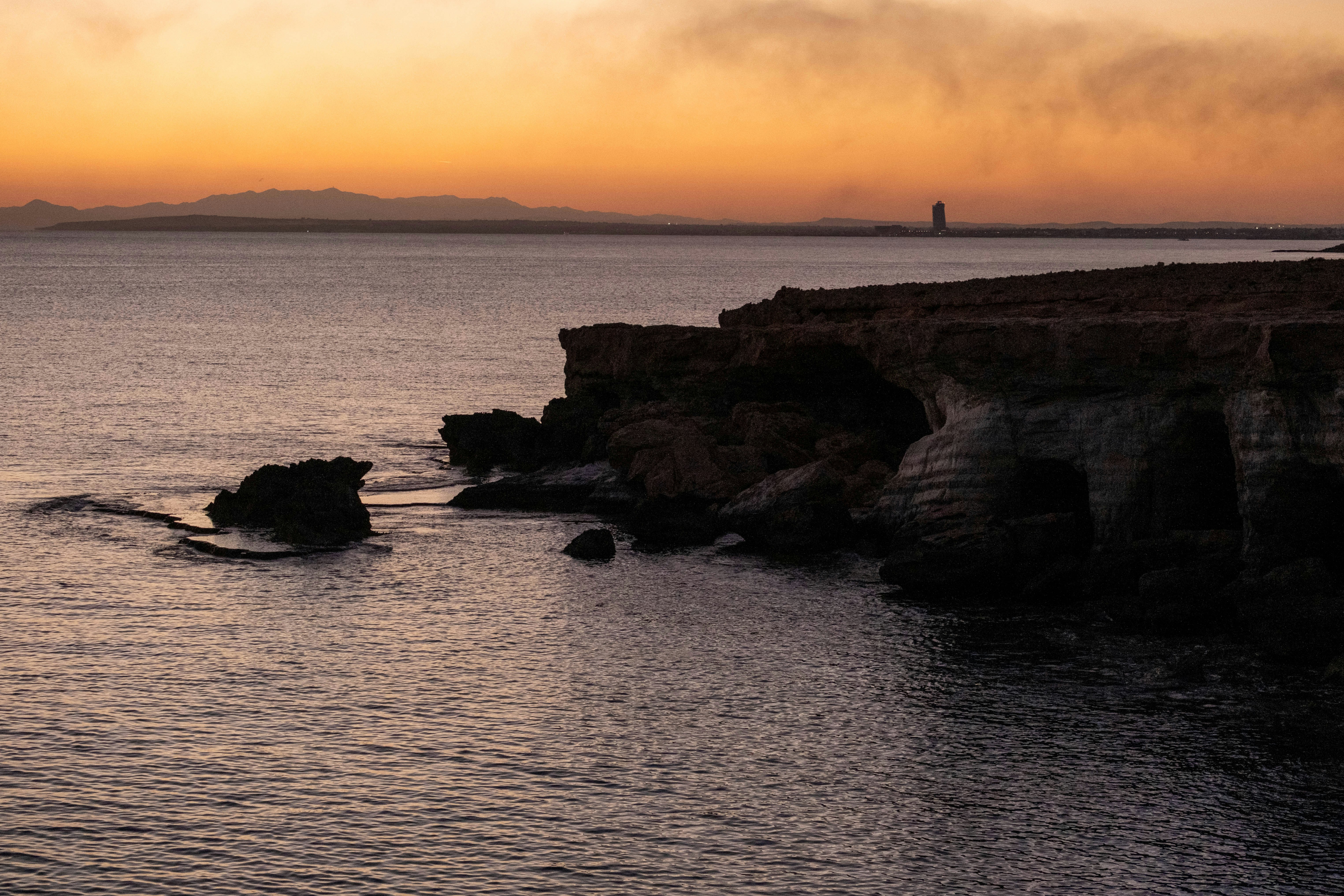 Horizon of Quiet Fire: Sunset Over Jagged Rocks and Distant Tower