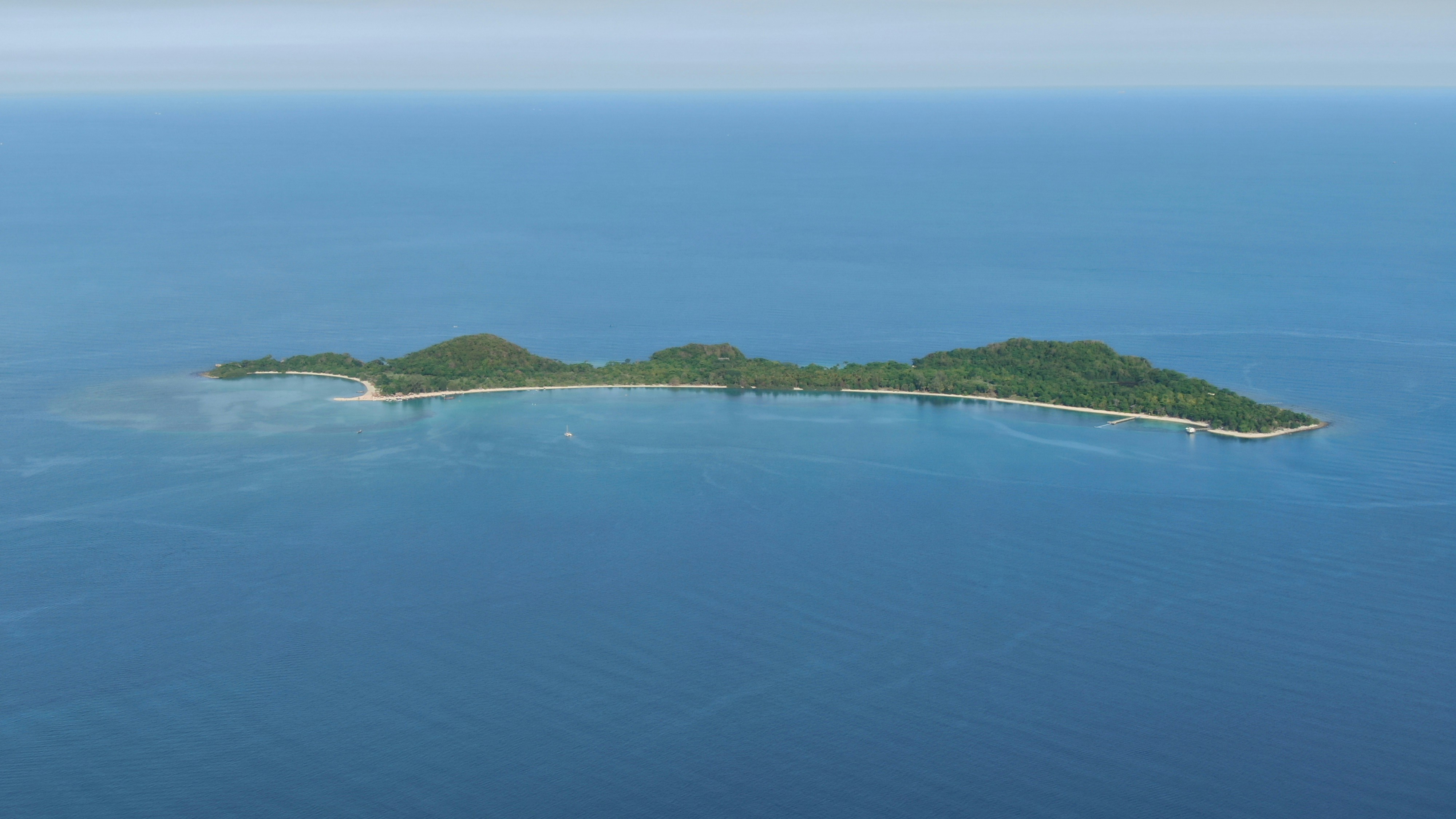 Aerial view of a secluded island surrounded by tranquil blue waters and lush greenery, showcasing nature's untouched beauty.