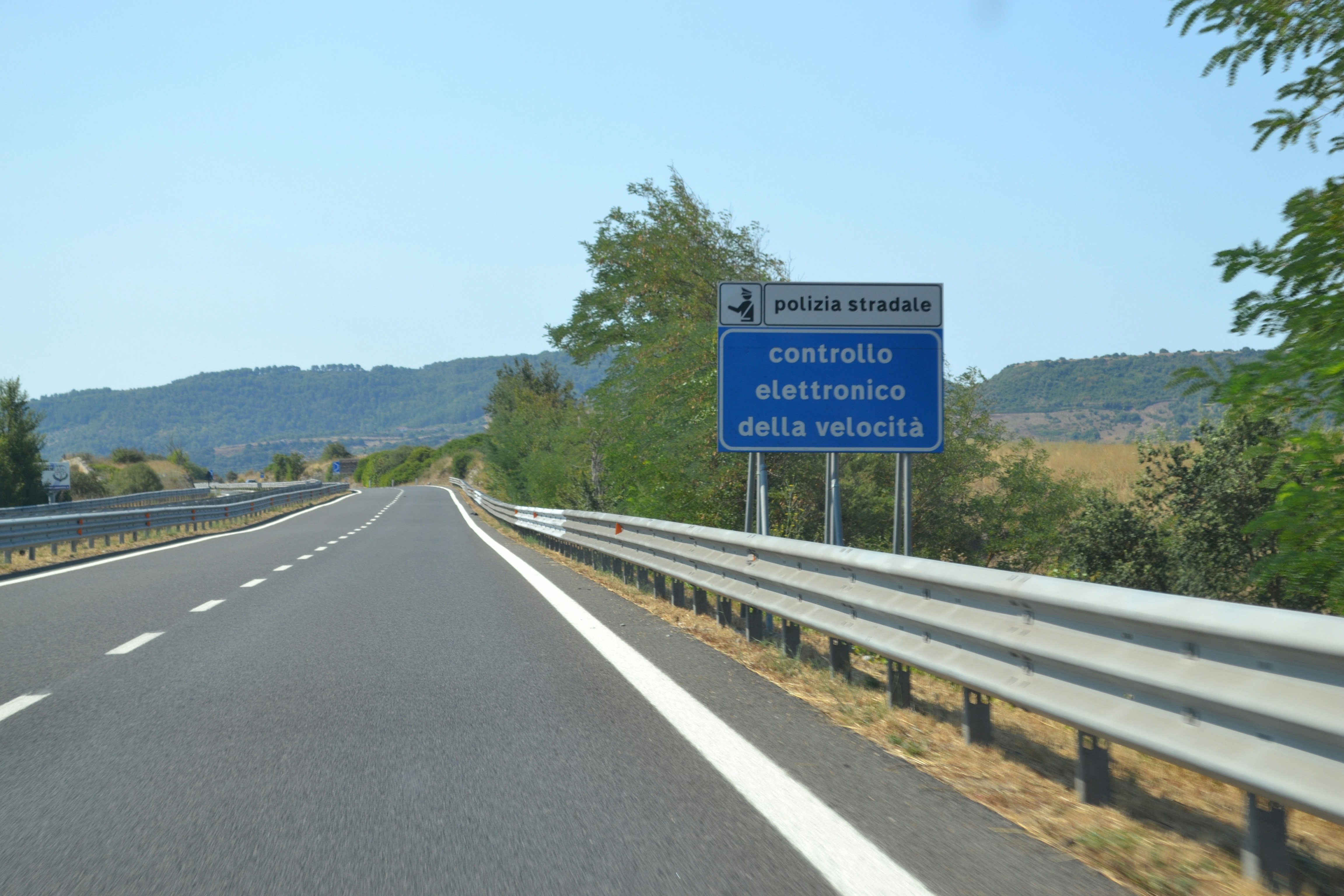 Road sign indicating speed control on a highway surrounded by lush greenery and rolling hills.