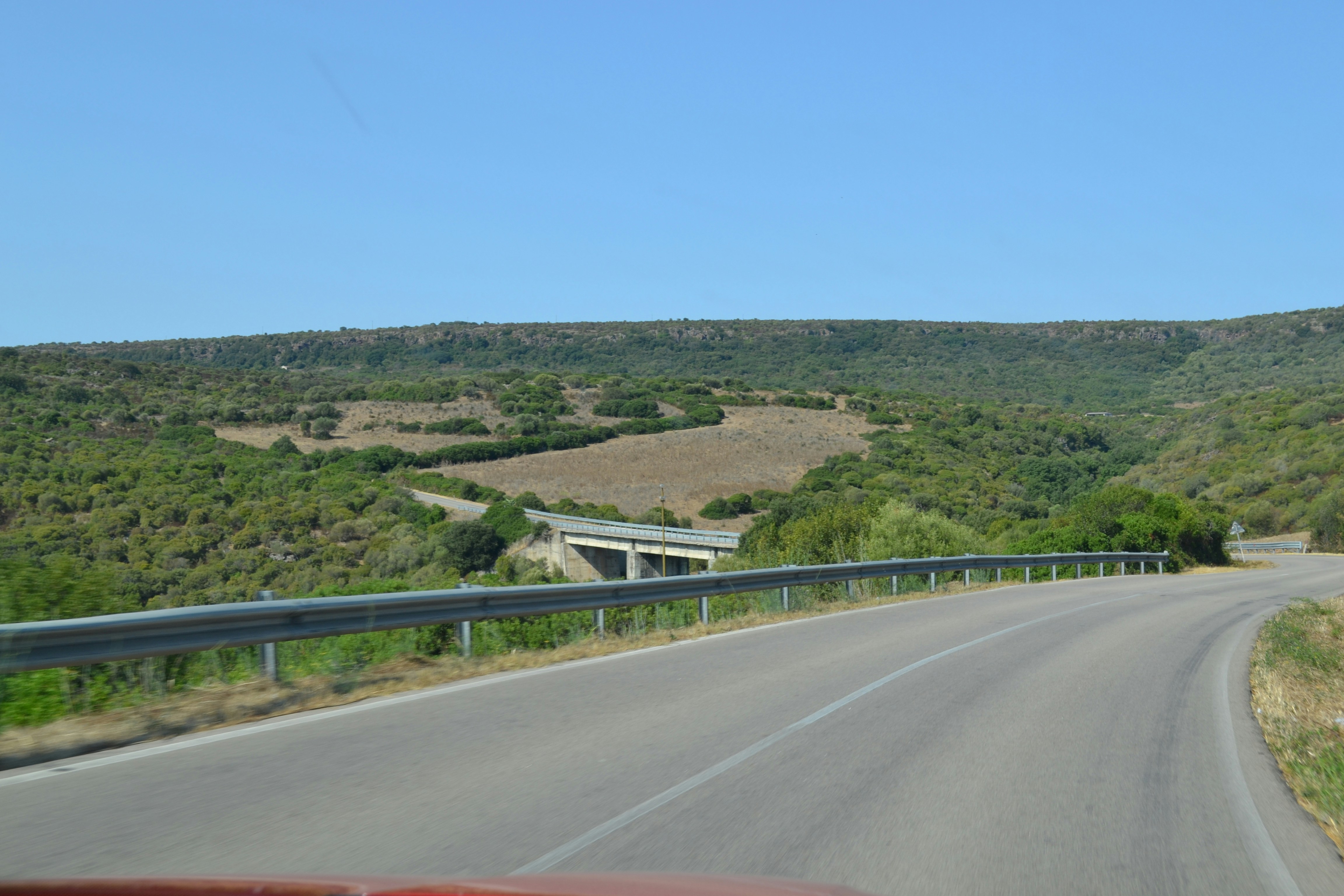 Curving road passes green hills under clear sky
