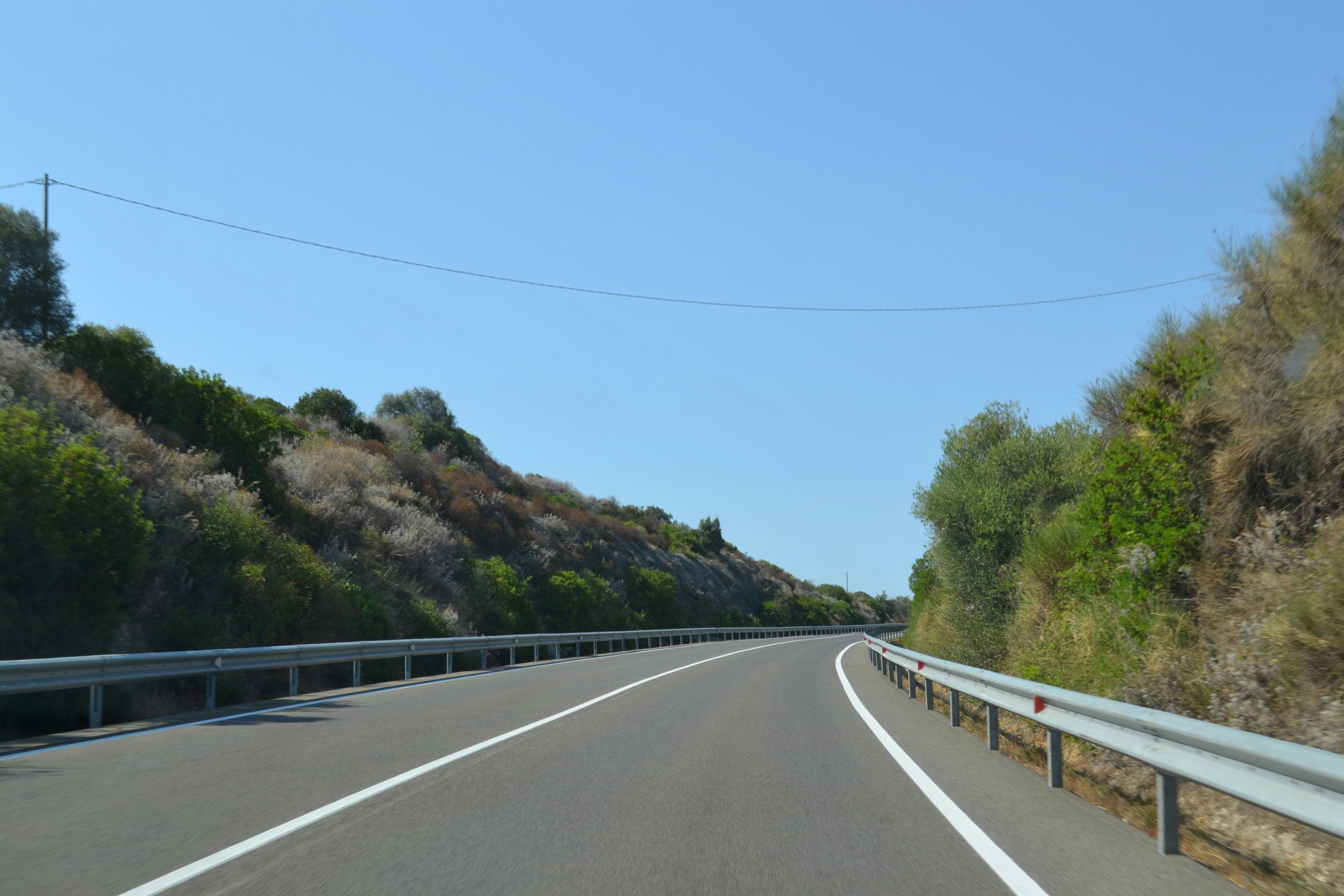 Curving road through dry, green landscape under clear sky.