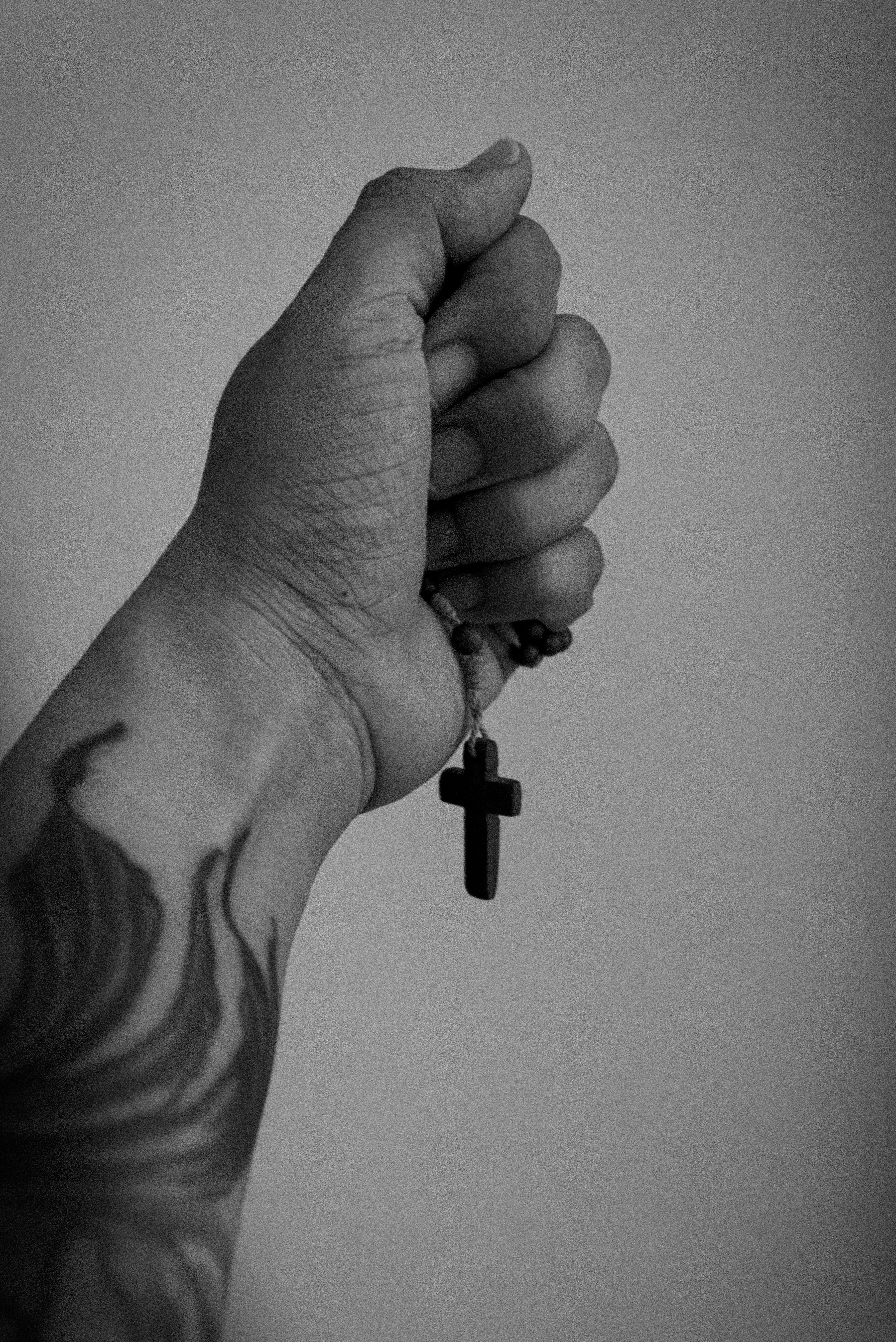 A hand holds a rosary with a cross.
