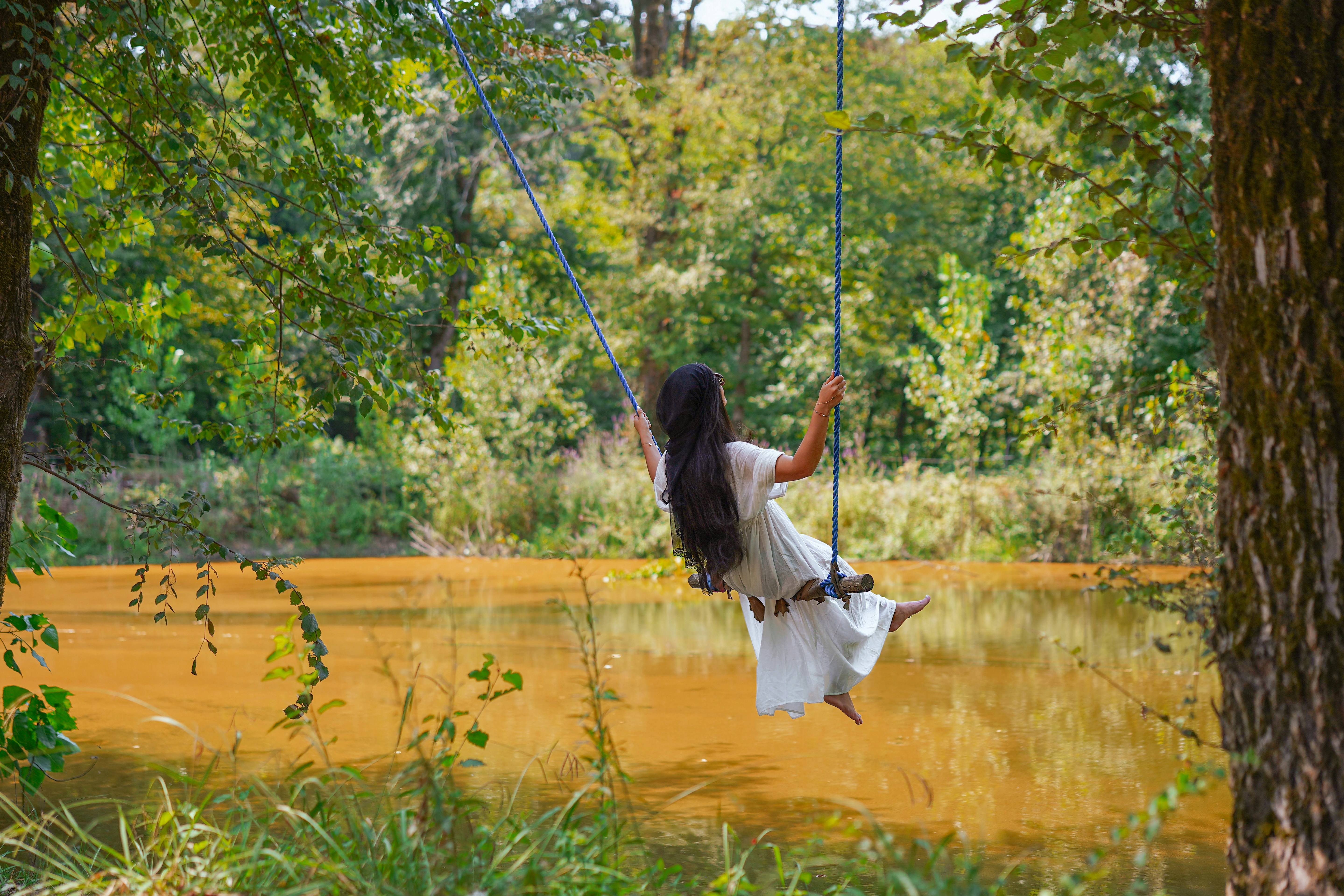 Woman in white dress swinging on a rope swing