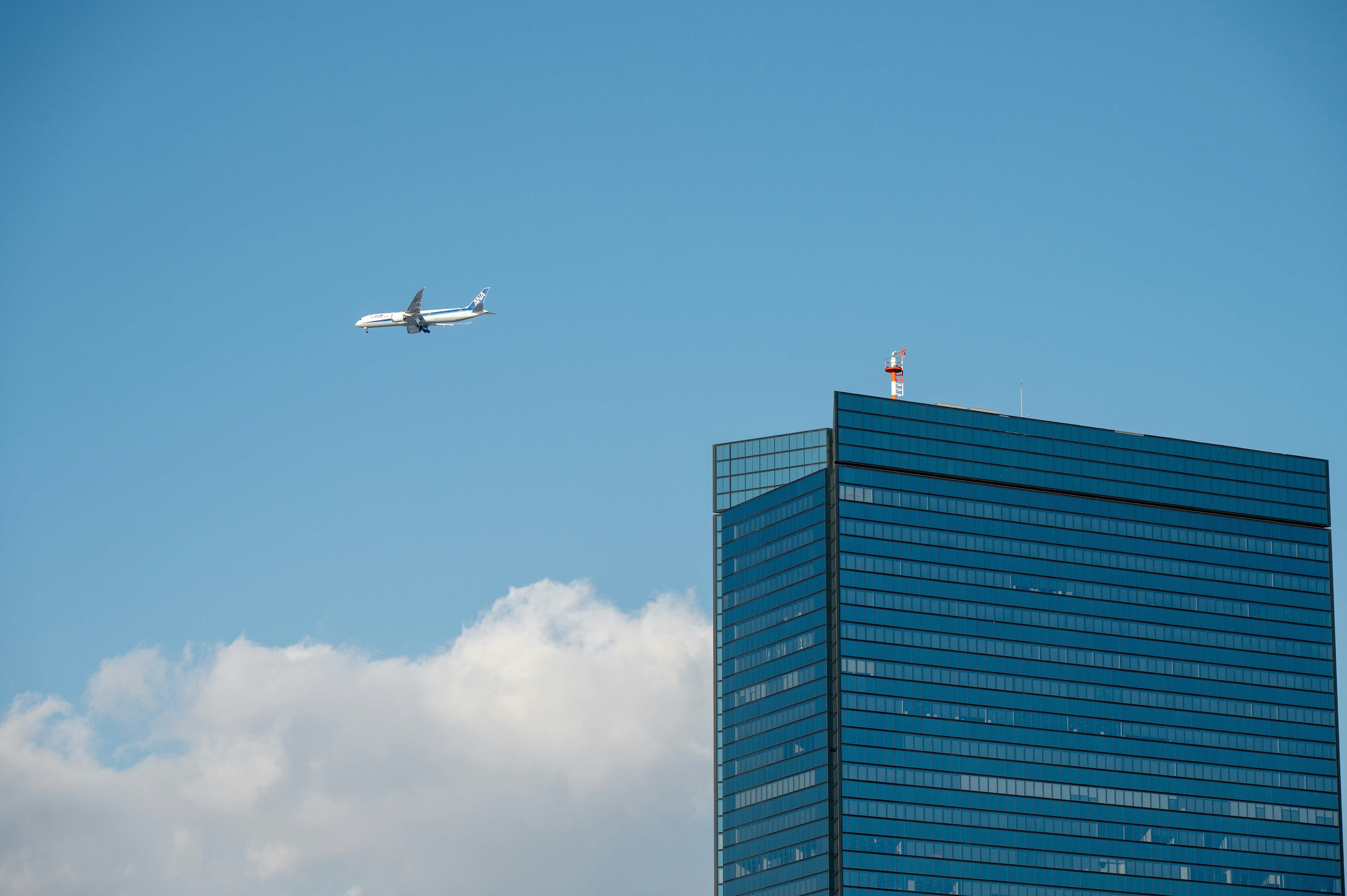 Airplane gliding through a clear blue sky above a modern glass skyscraper, showcasing the harmony of urban architecture and aviation.