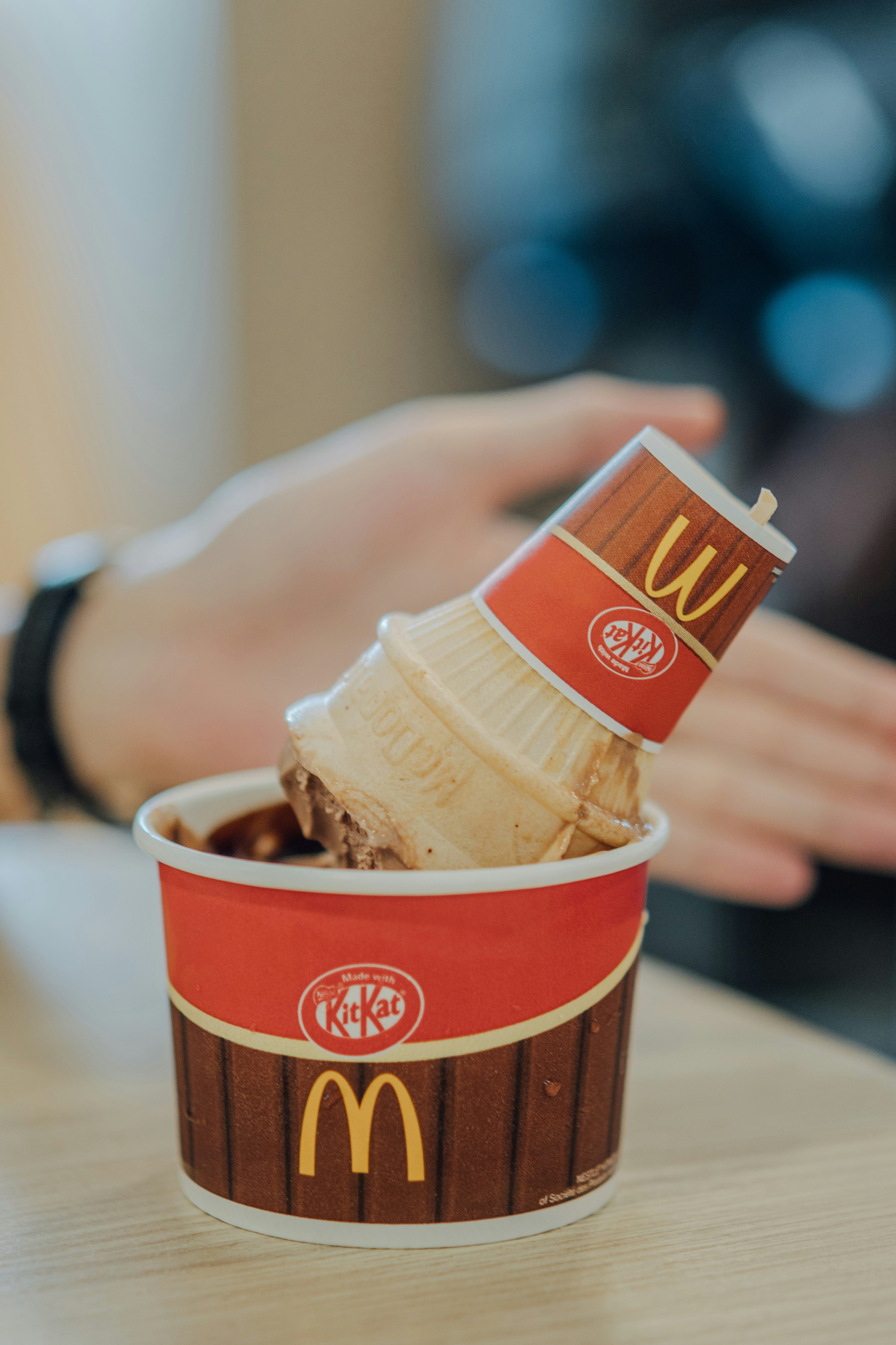 Chocolate ice cream topped with a KitKat cone inside a McDonald's cup, with a hand reaching for it.