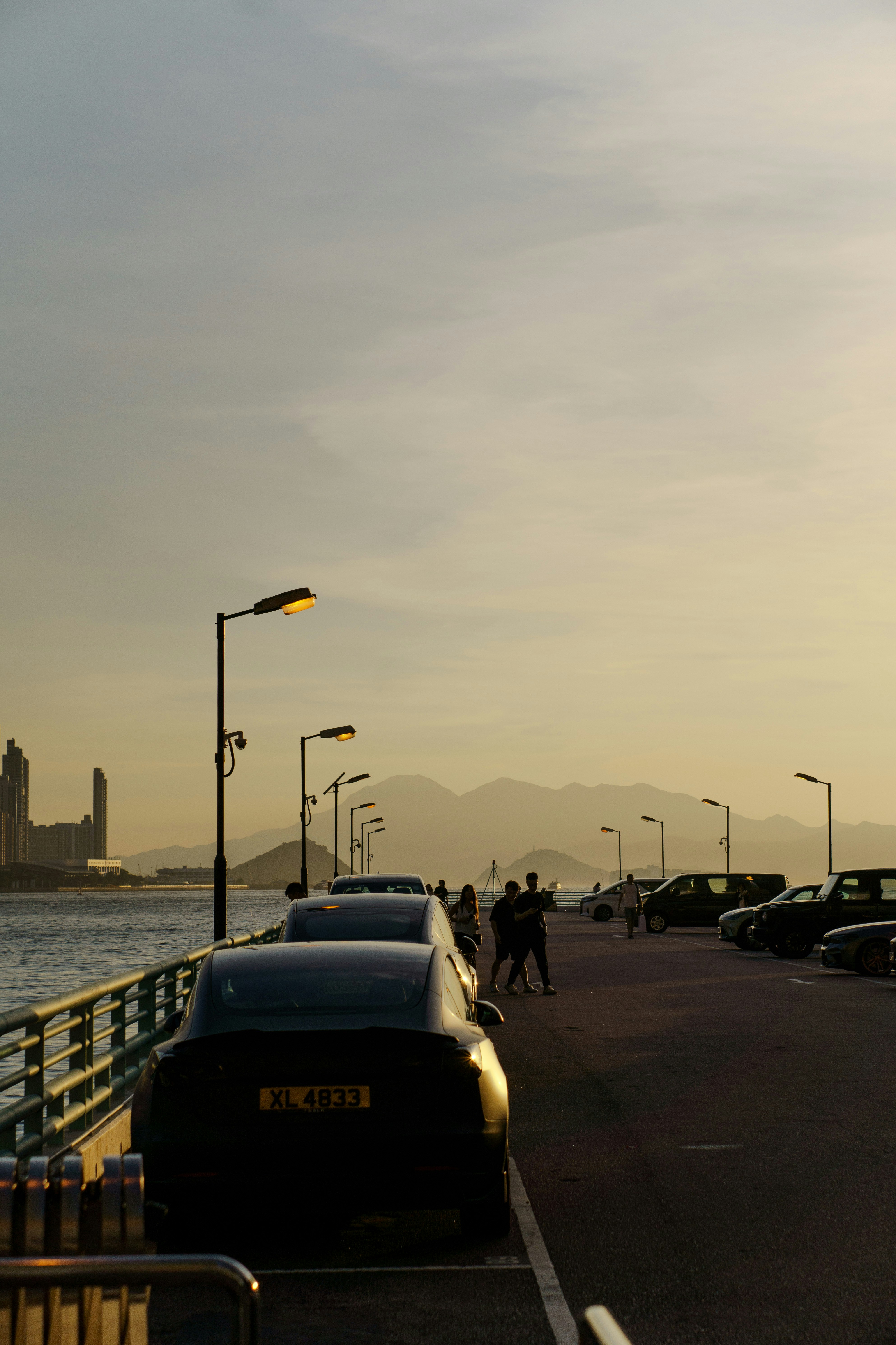 Cars parked along a waterfront promenade at sunset.