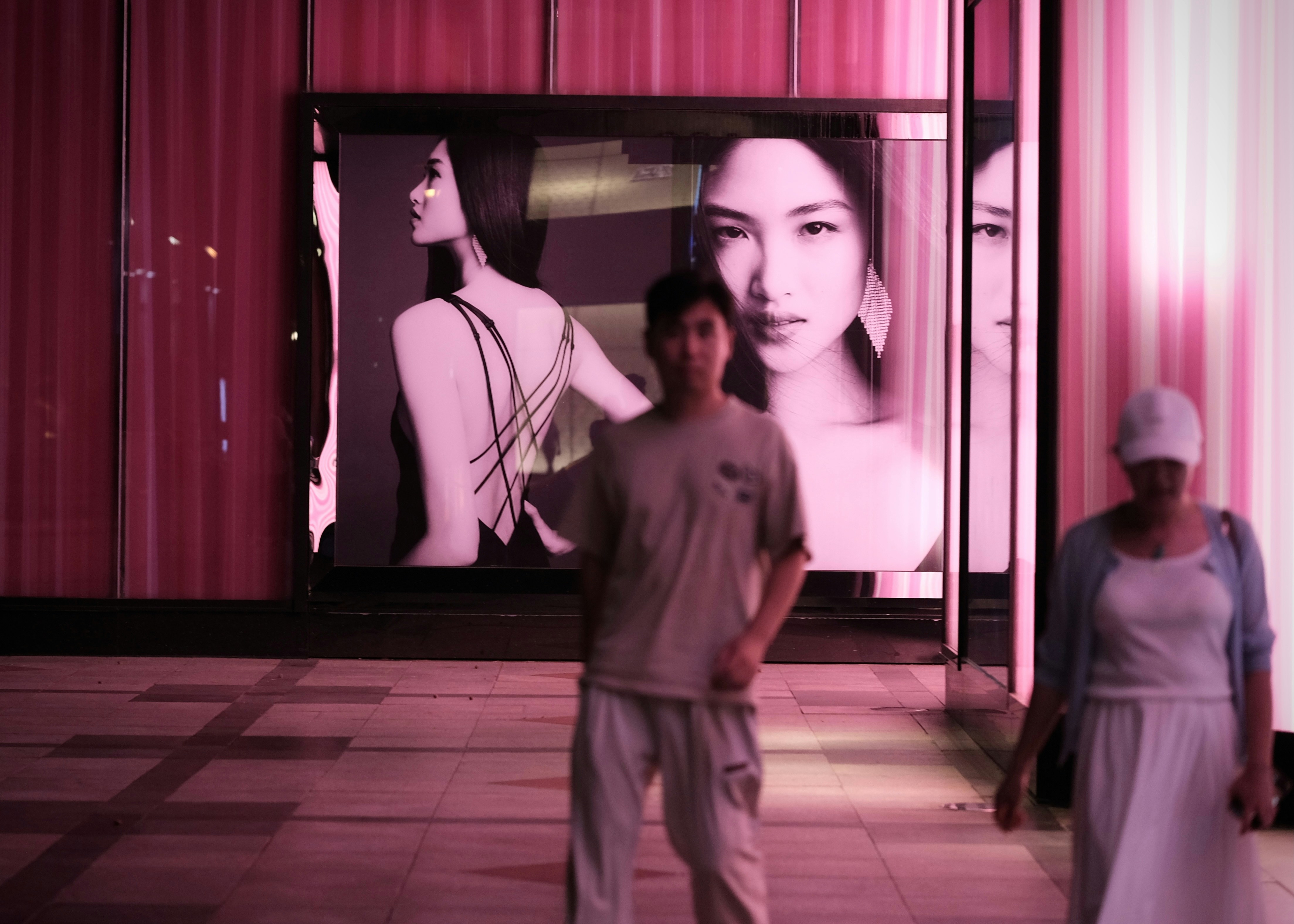 Two people stand before a large screen displaying a black and white portrait.