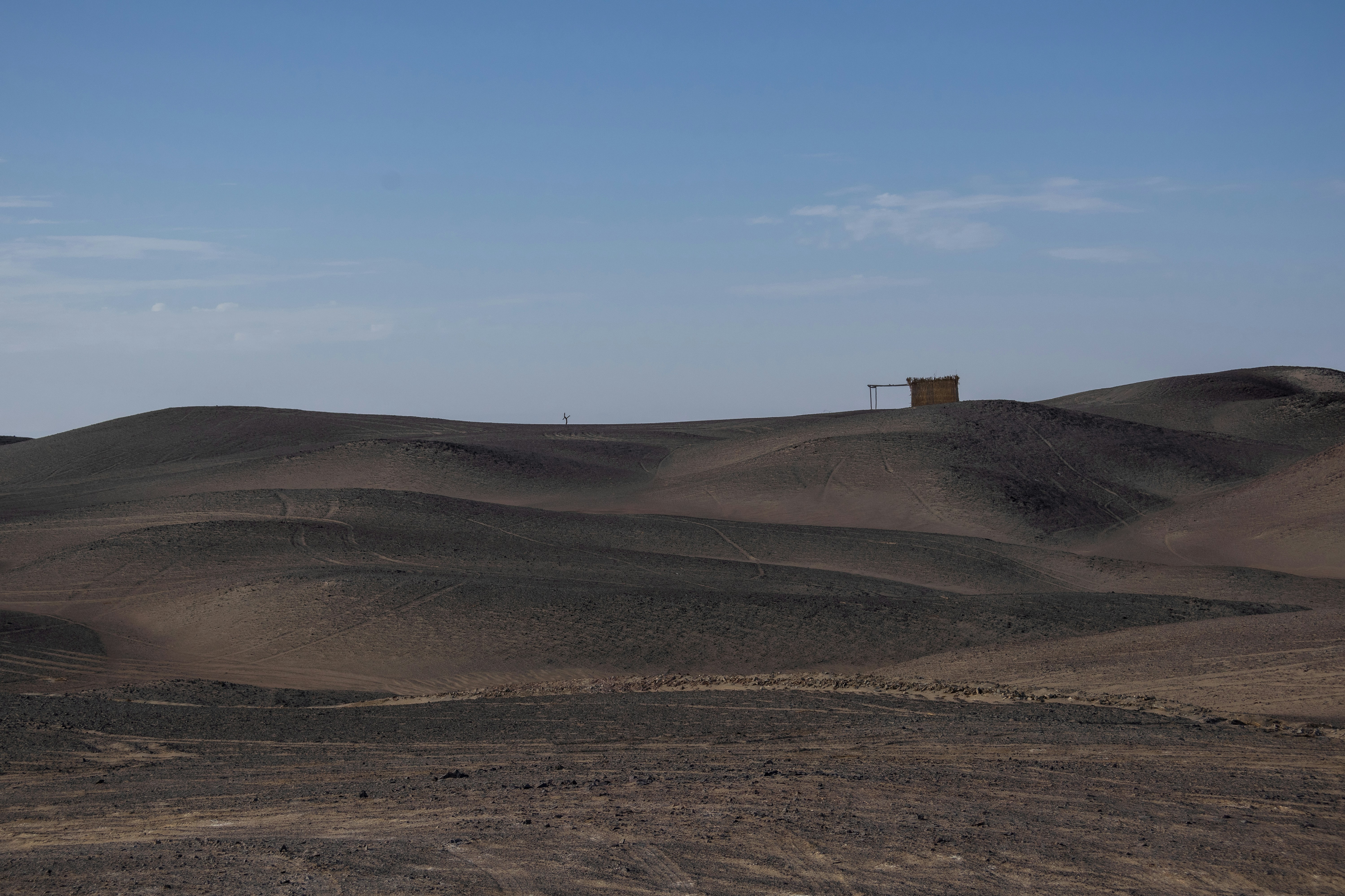 A lone structure stands on a barren, sandy hill.