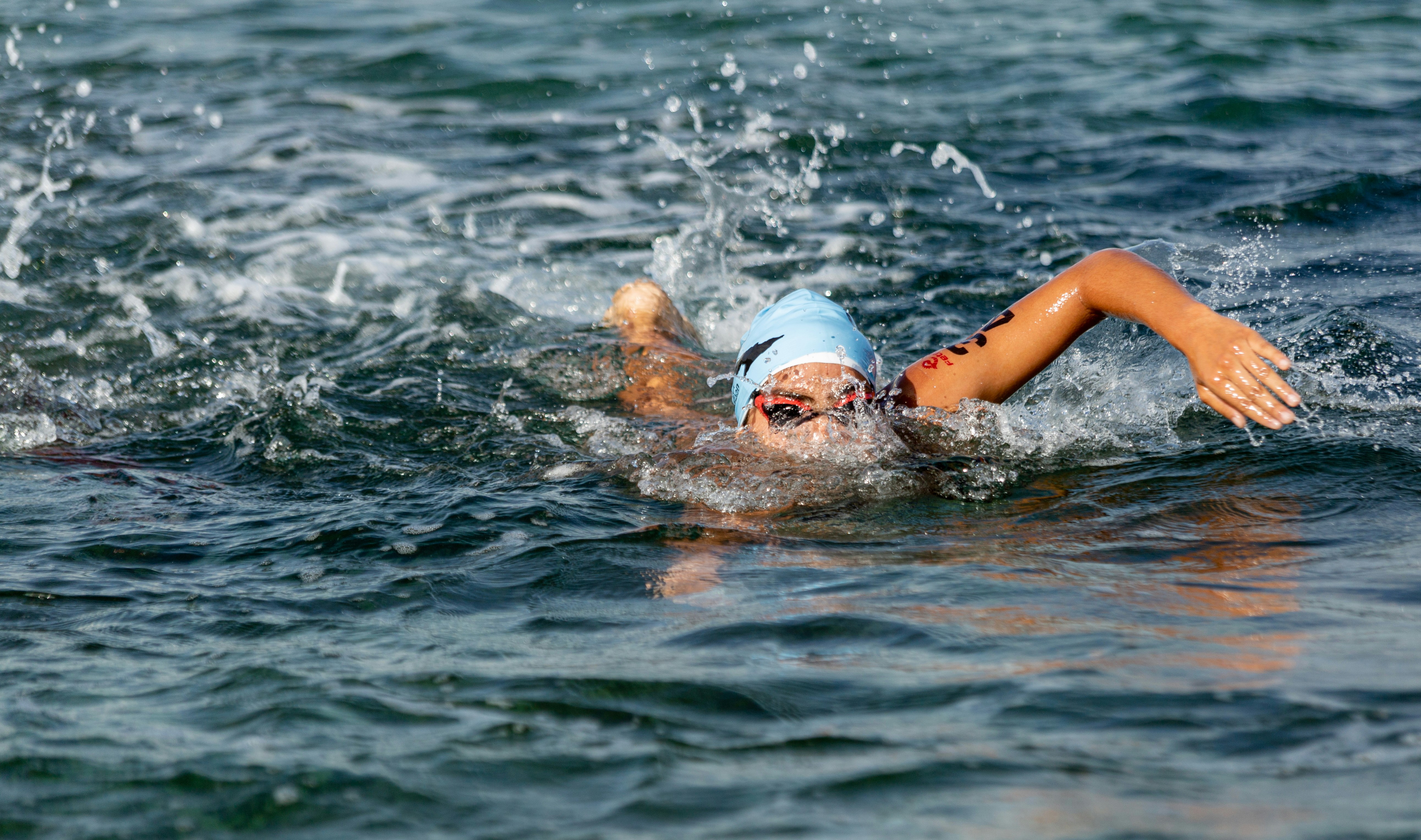 Swimmer with white cap strokes through dark water