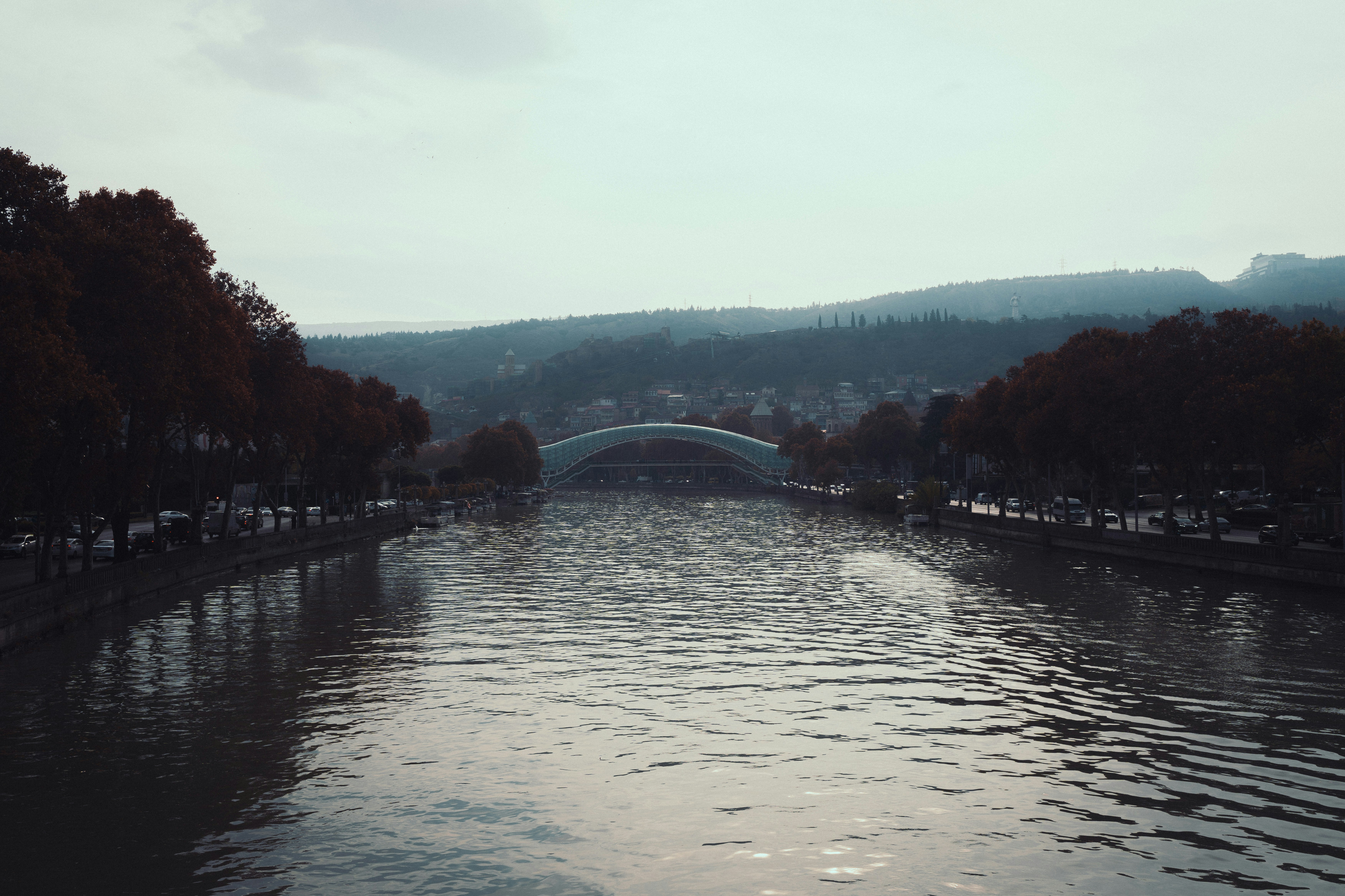 Calm river with trees and a bridge in distance.