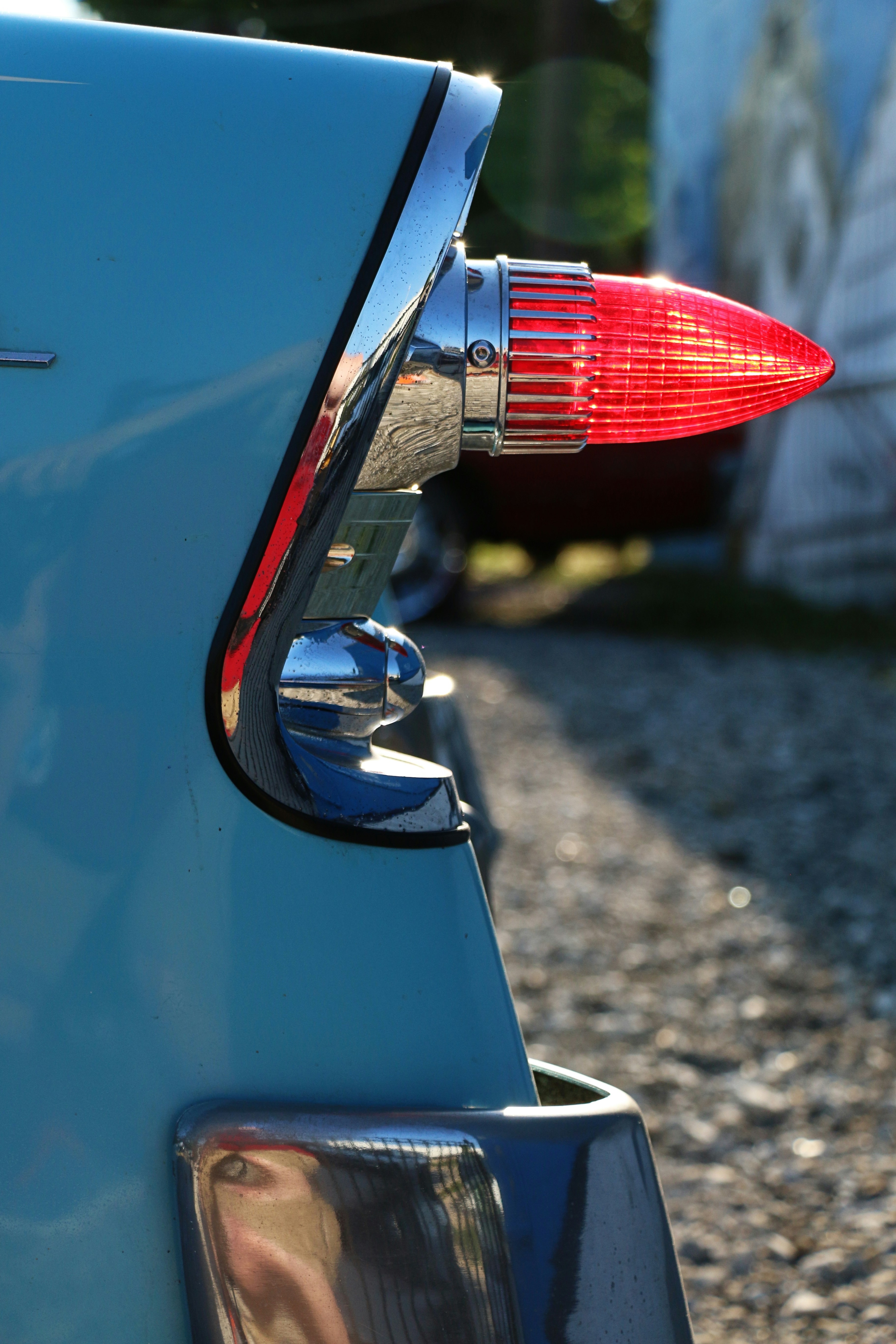 Close-up of a classic car's tail light, showcasing its vibrant red lens and sleek chrome details against a blurred background.