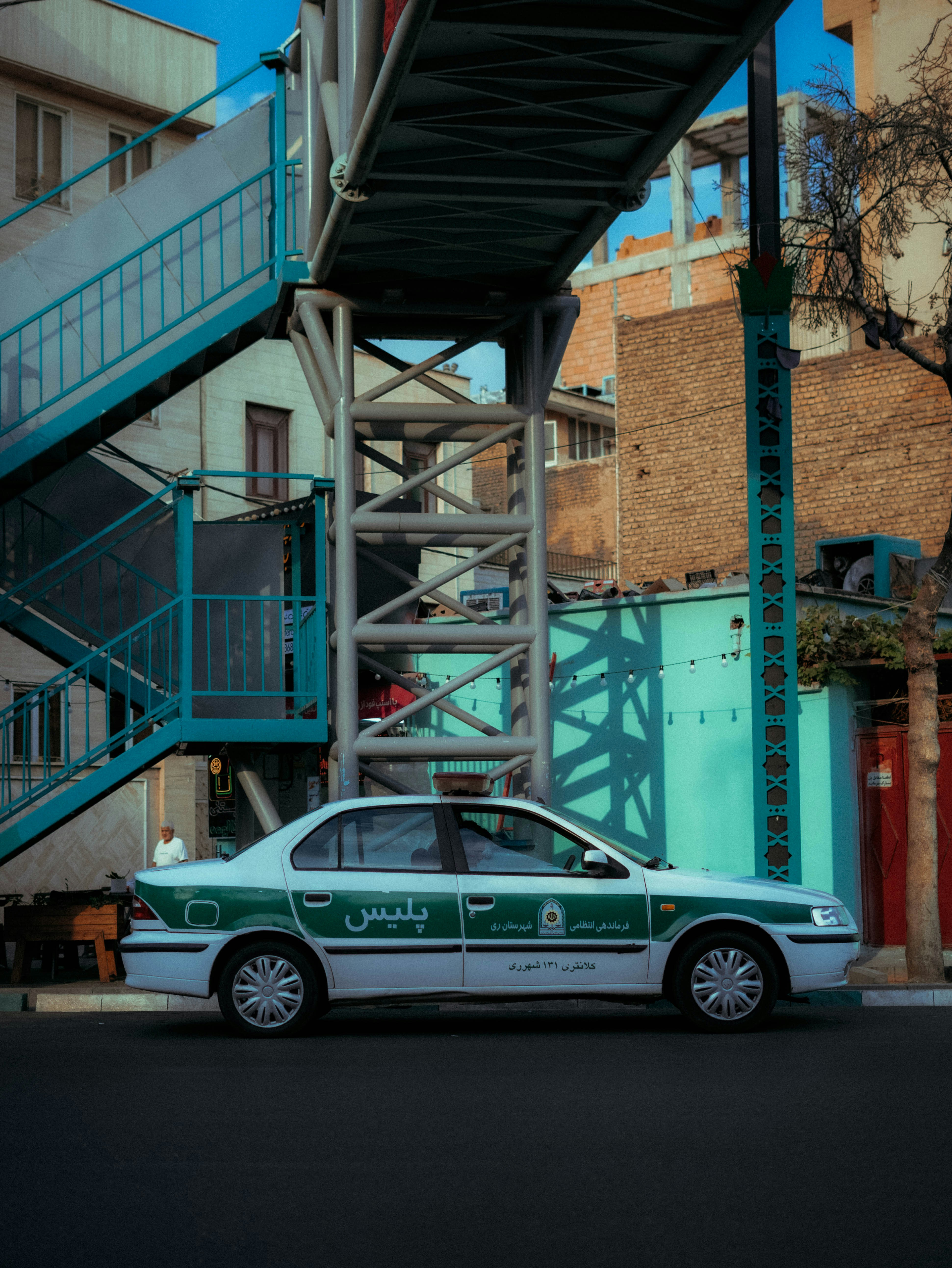 Blue stairway overpass frames a teal taxi beneath urban lattice