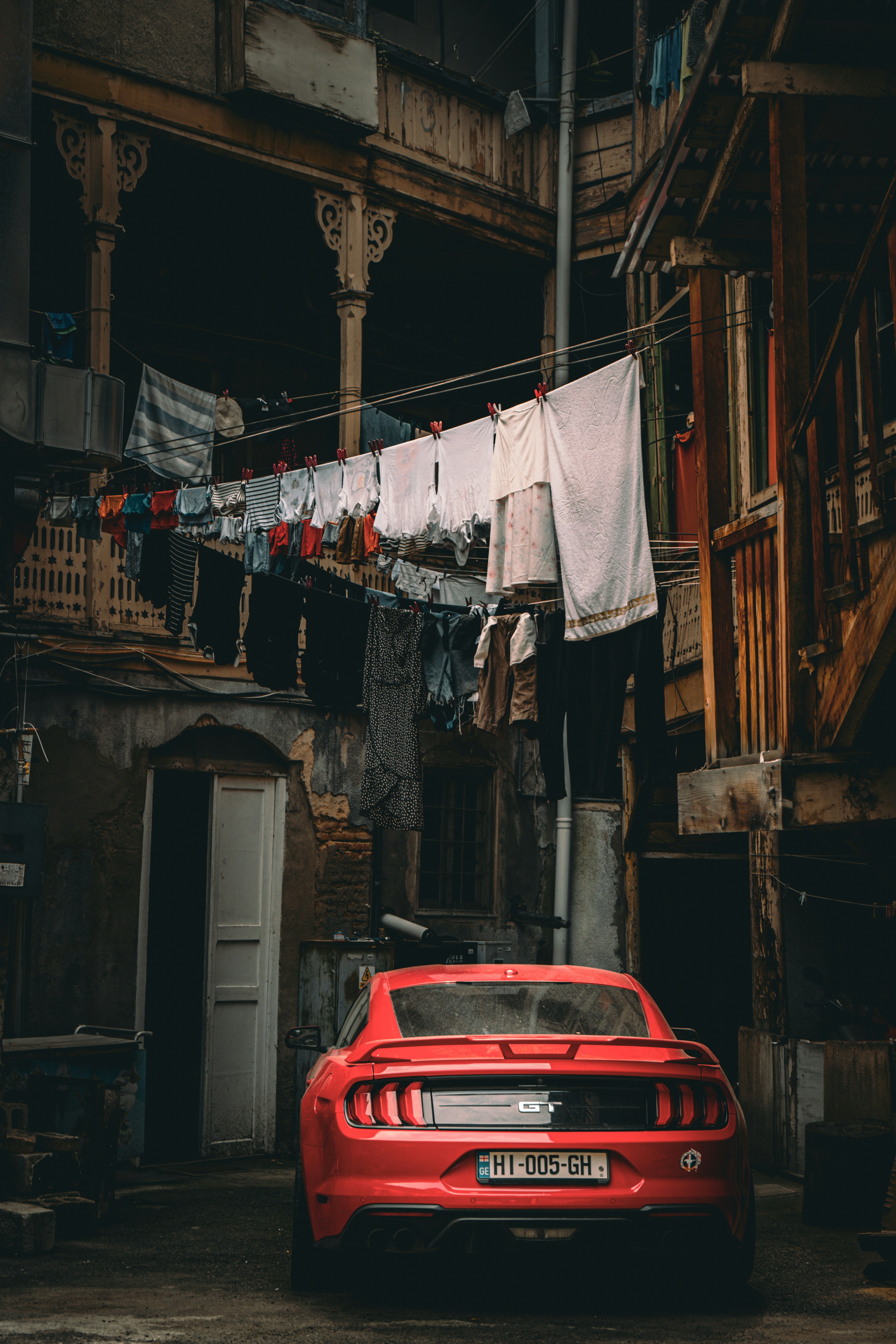 Red car parked in a narrow alley with laundry hanging.