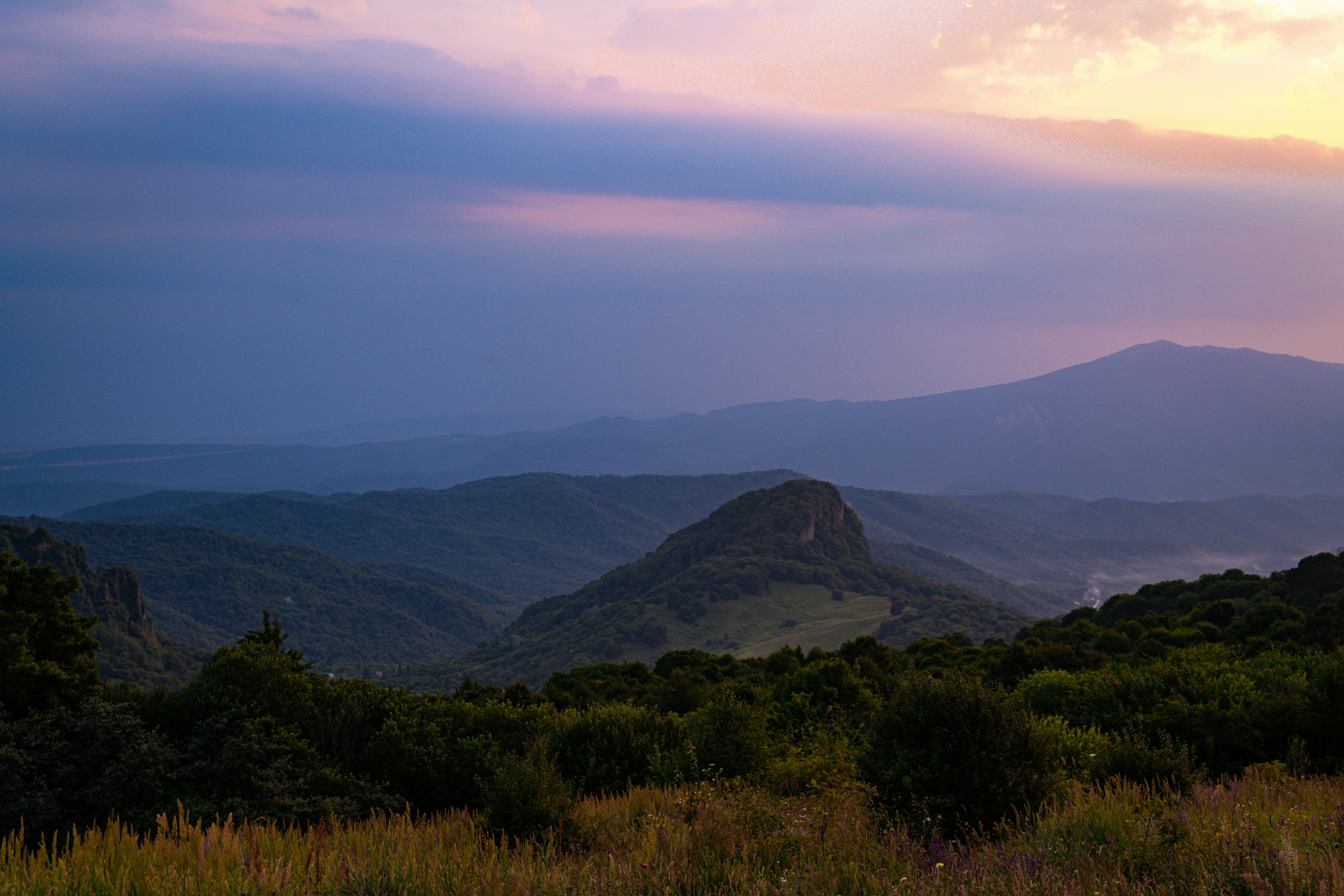 Hills and mountains under a cloudy sky at sunset.