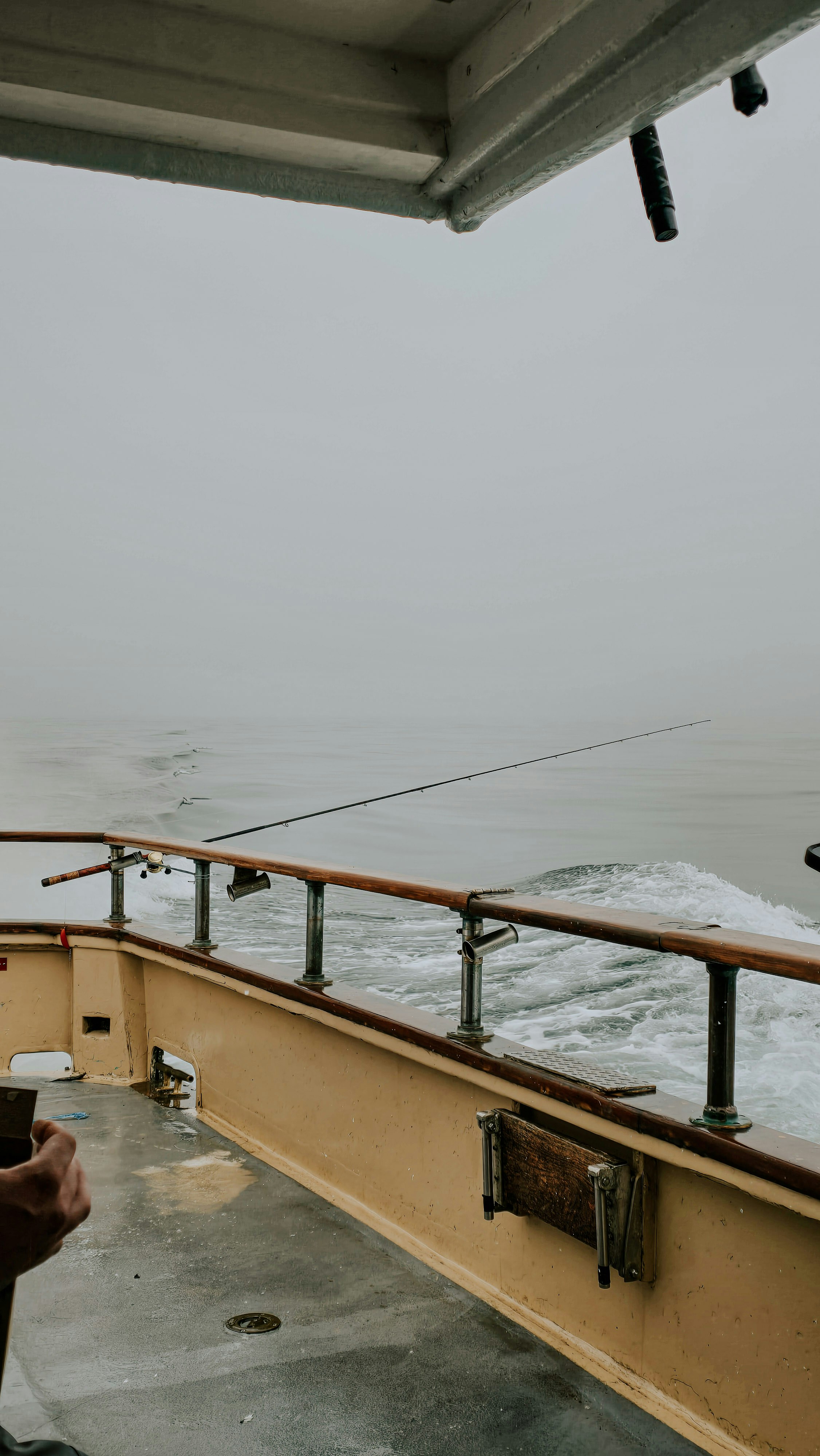 A fishing boat navigating through a foggy sea, with a fishing rod poised for action. The calm waters reflect the muted tones of the misty atmosphere.