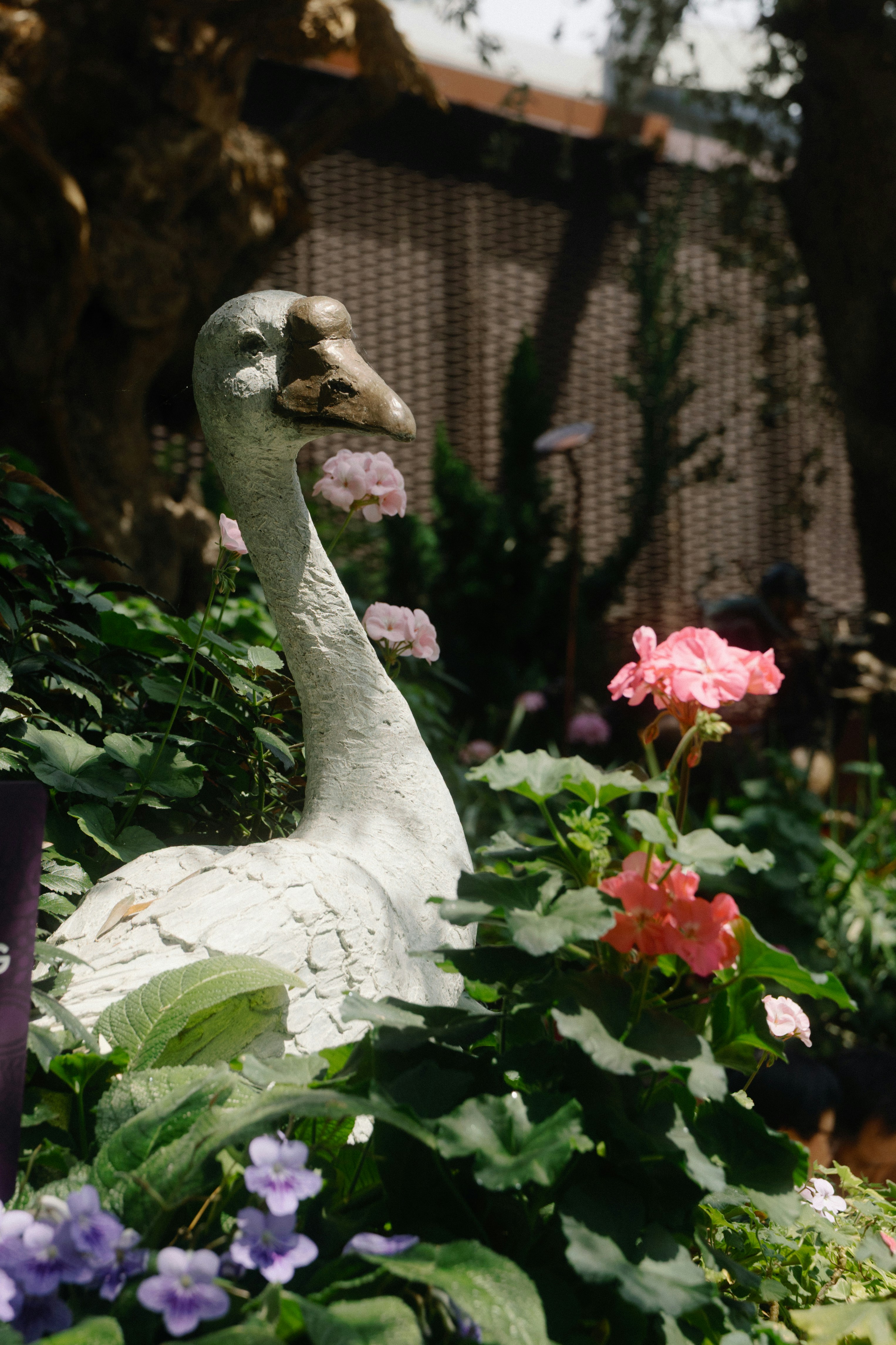 A charming ceramic goose statue surrounded by vibrant flowers, adding a playful touch to the garden scene.
