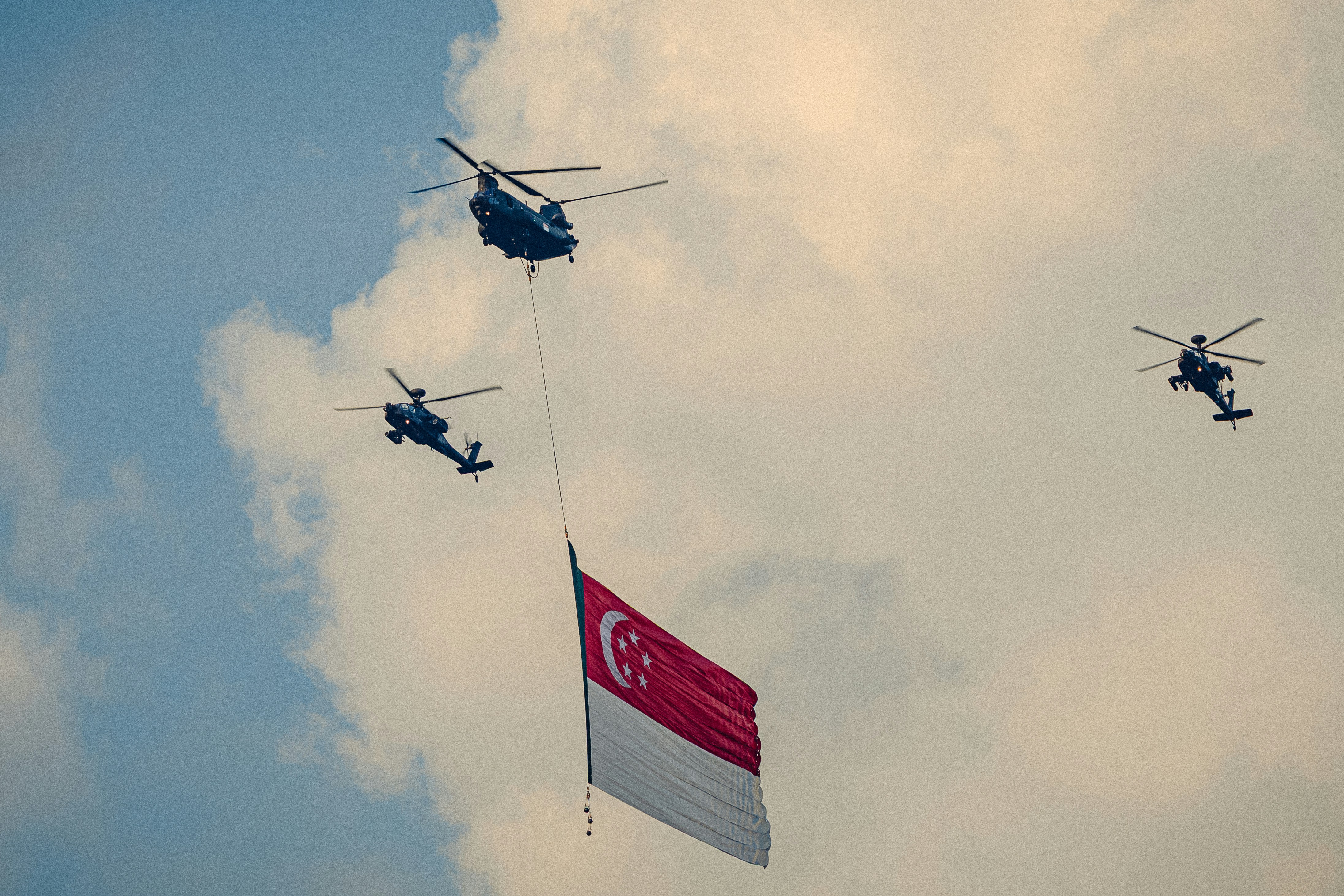 Helicopters fly past the singapore flag in the sky.