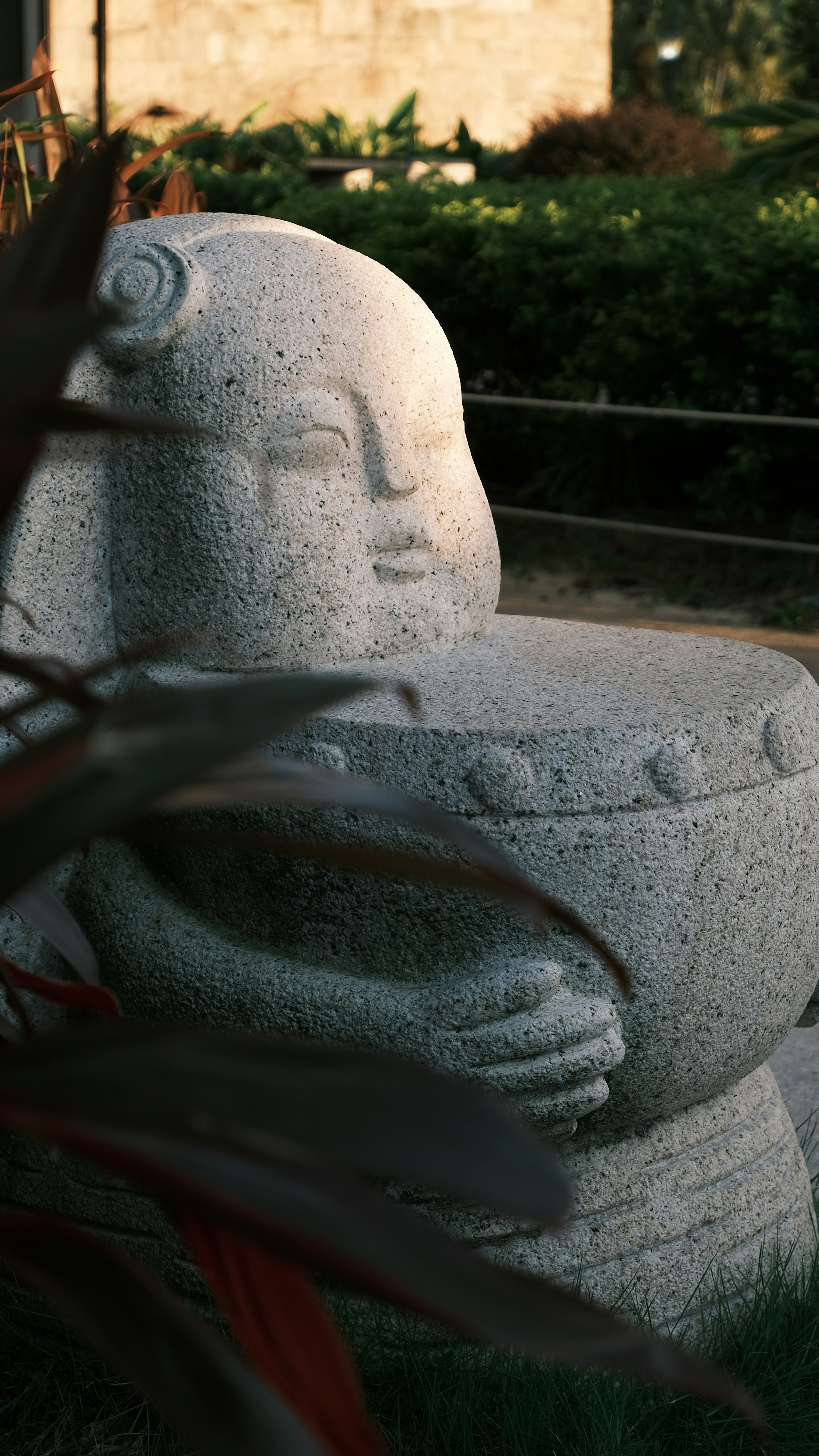 Stone statue holding a bowl in a garden