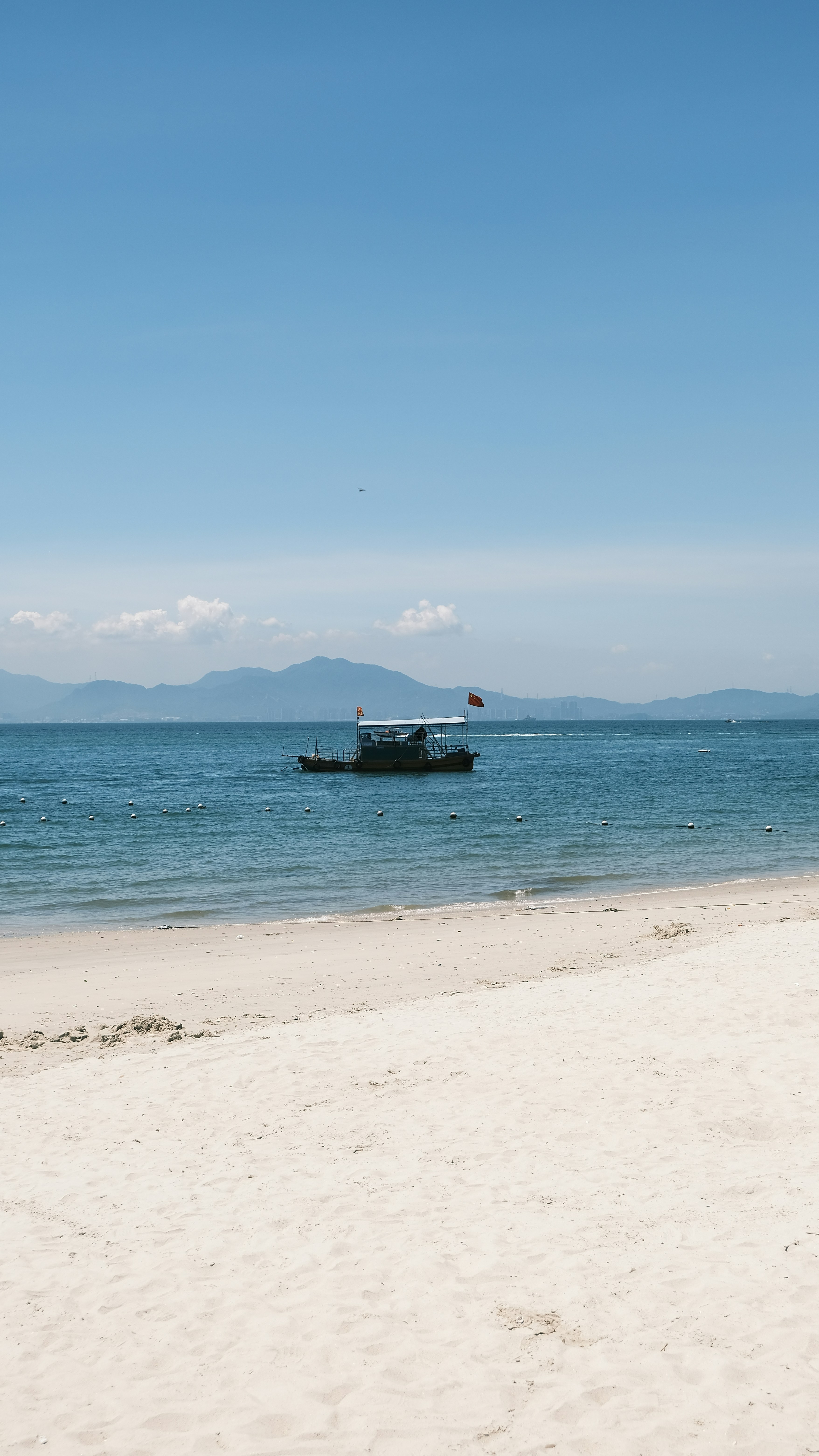 A boat floats on the calm ocean near a sandy beach.