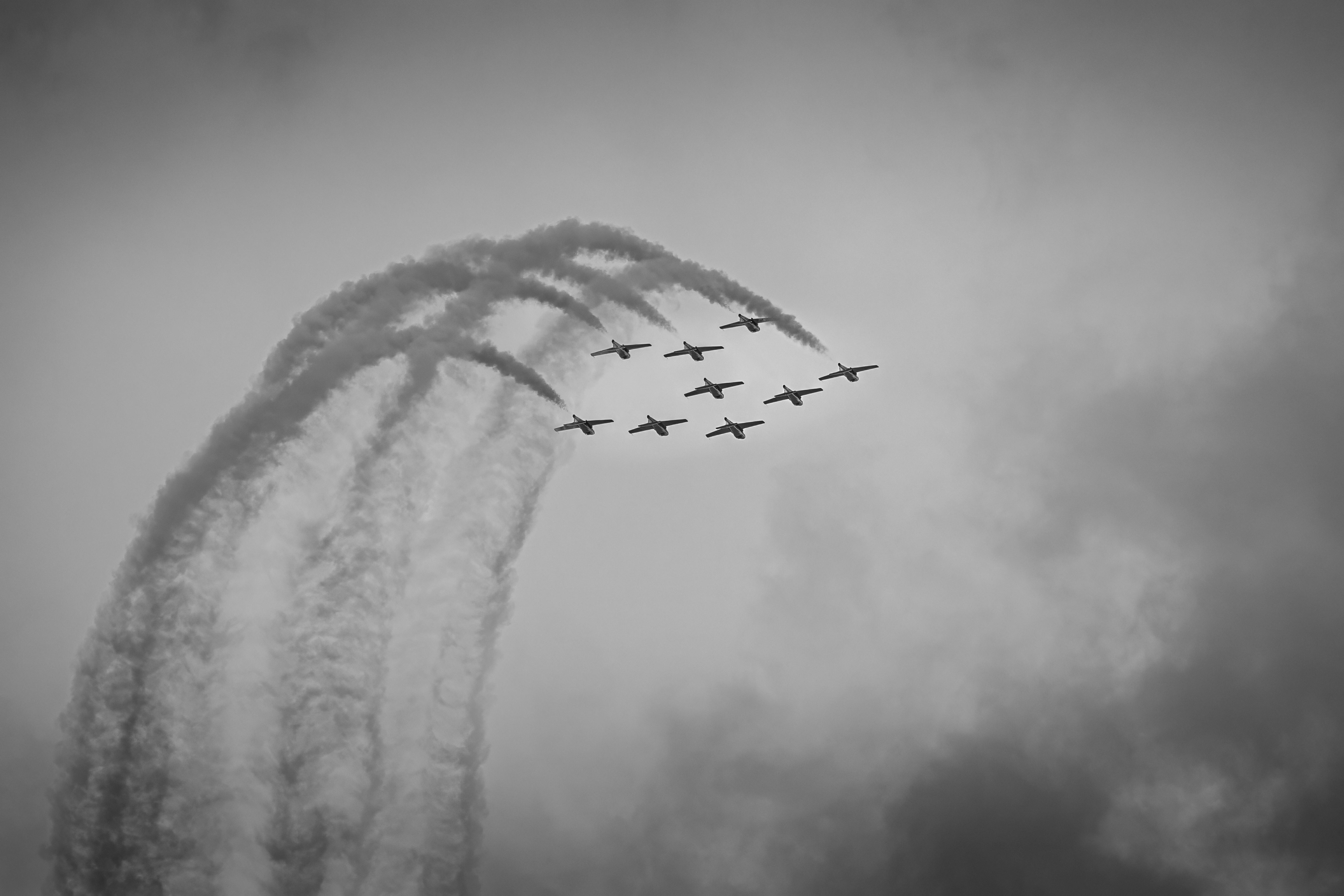 Formation of jets performing a synchronized aerial display, leaving trails of smoke against a cloudy sky.