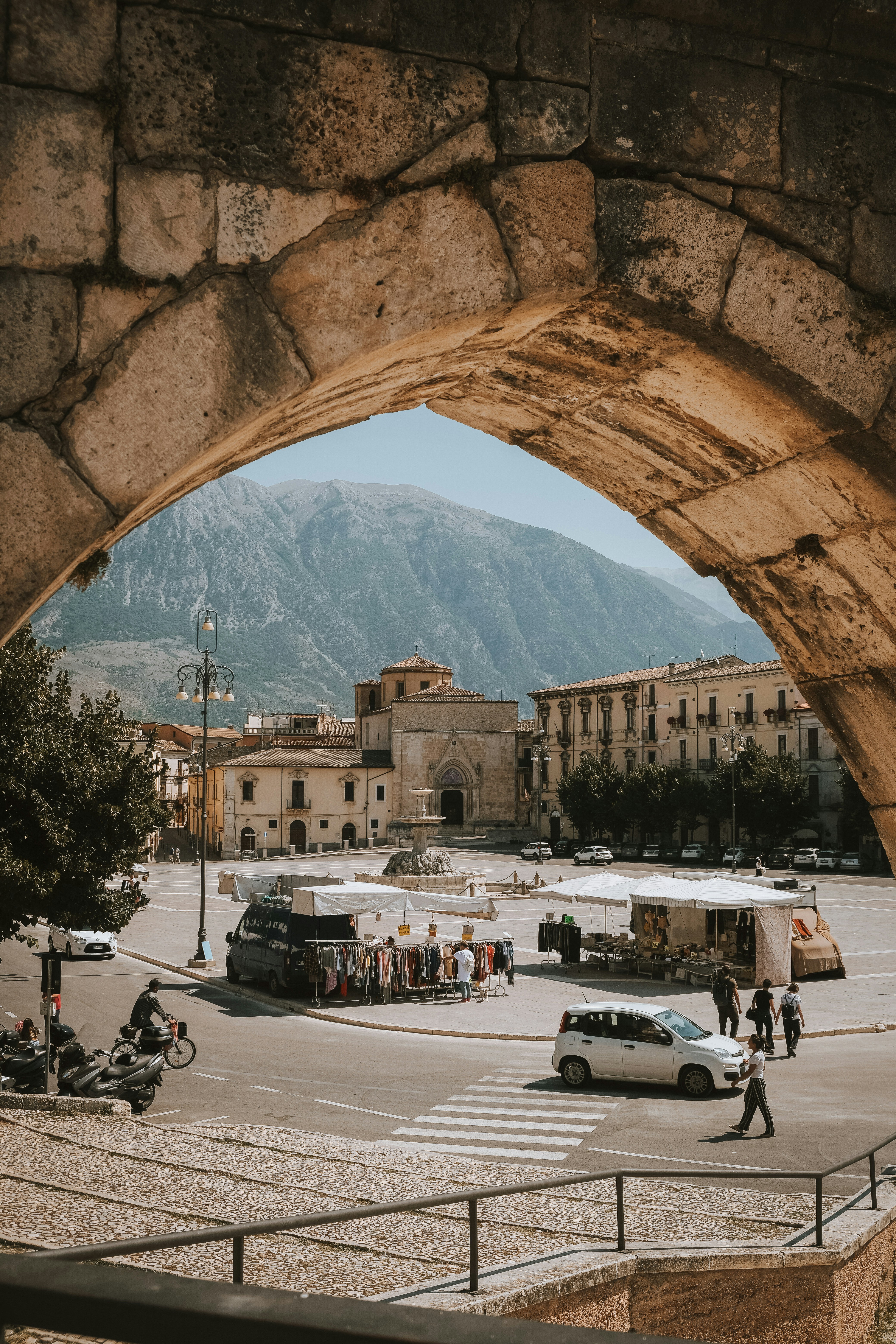 Sulmona , Abruzzo (Italy) | Stone archway frames a european town square with mountains.