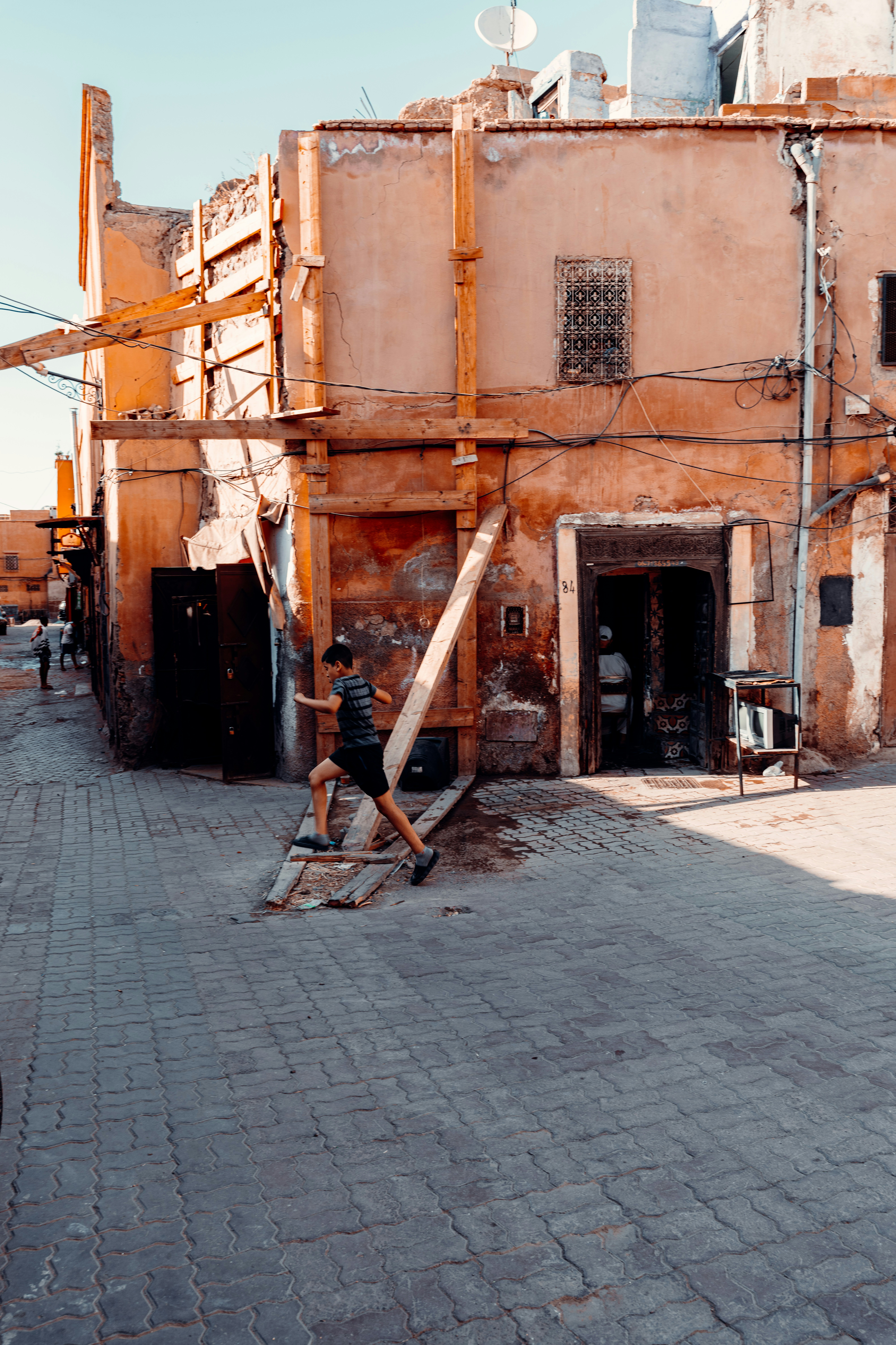 A young boy navigates a narrow street in a vibrant medina, showcasing the blend of traditional architecture and daily activities. The warm tones of the buildings add to the scene's charm.