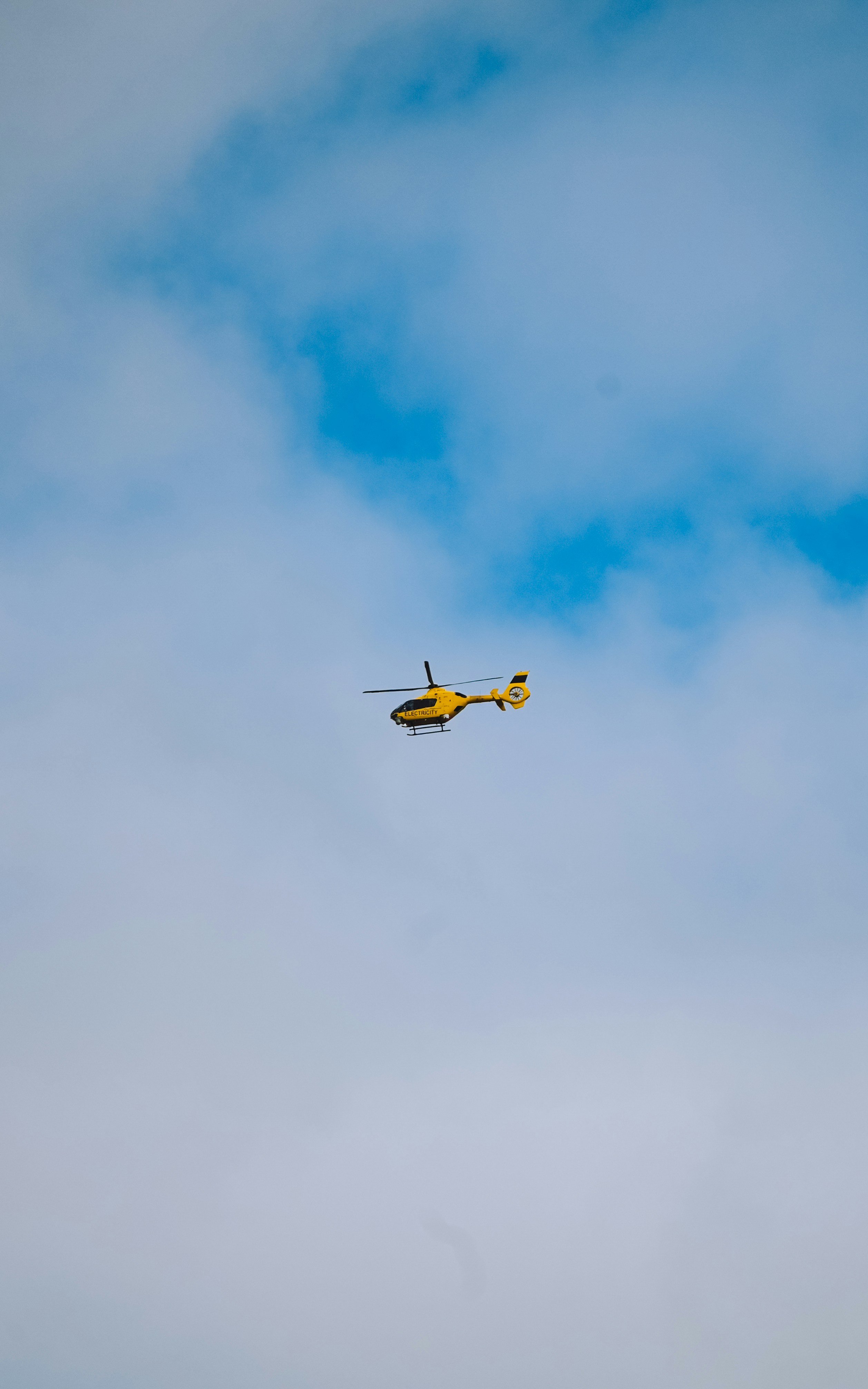 Yellow helicopter flying in a cloudy blue sky
