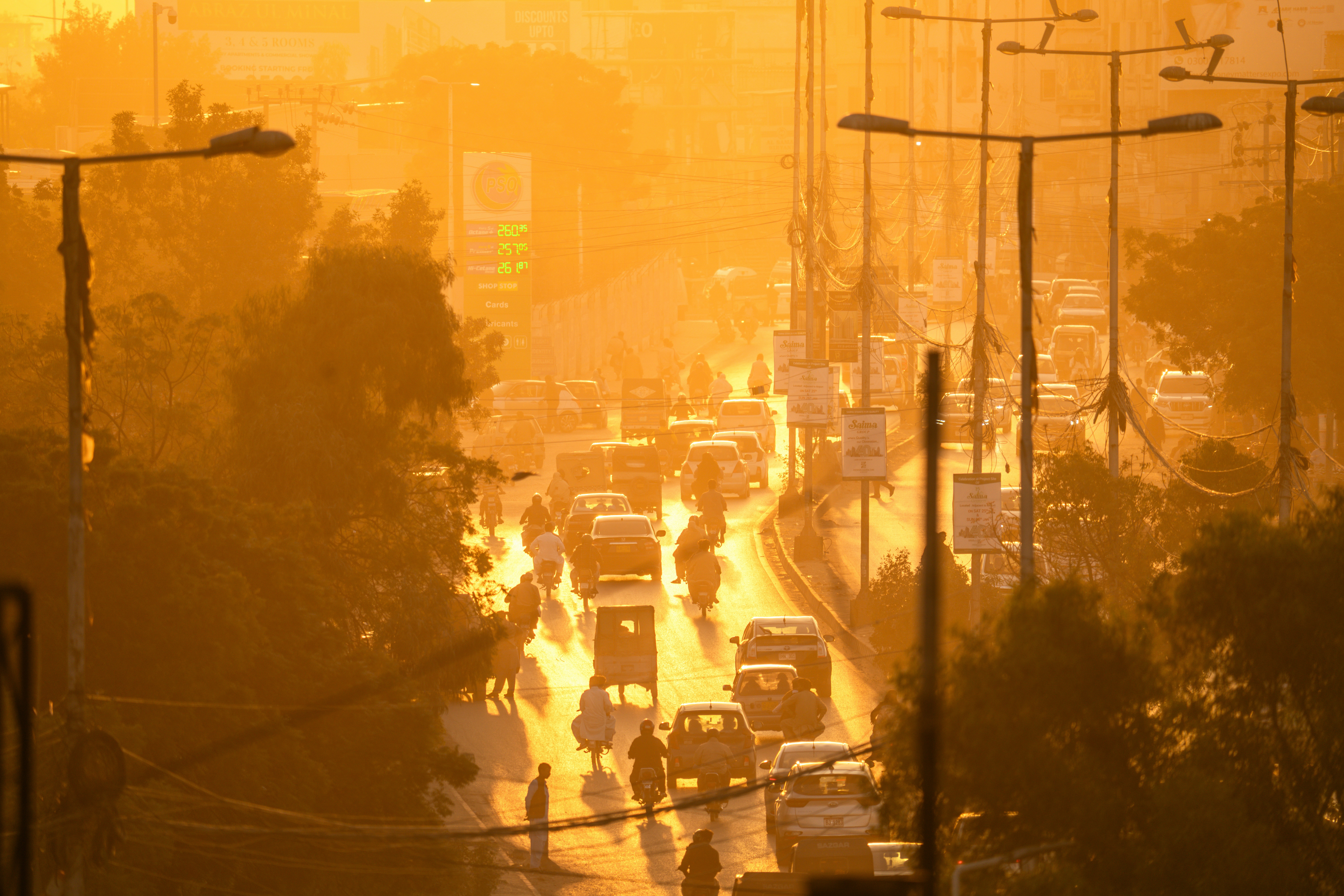 Vehicles and pedestrians navigate a busy street bathed in warm golden light during sunset, highlighting the hustle of urban life.