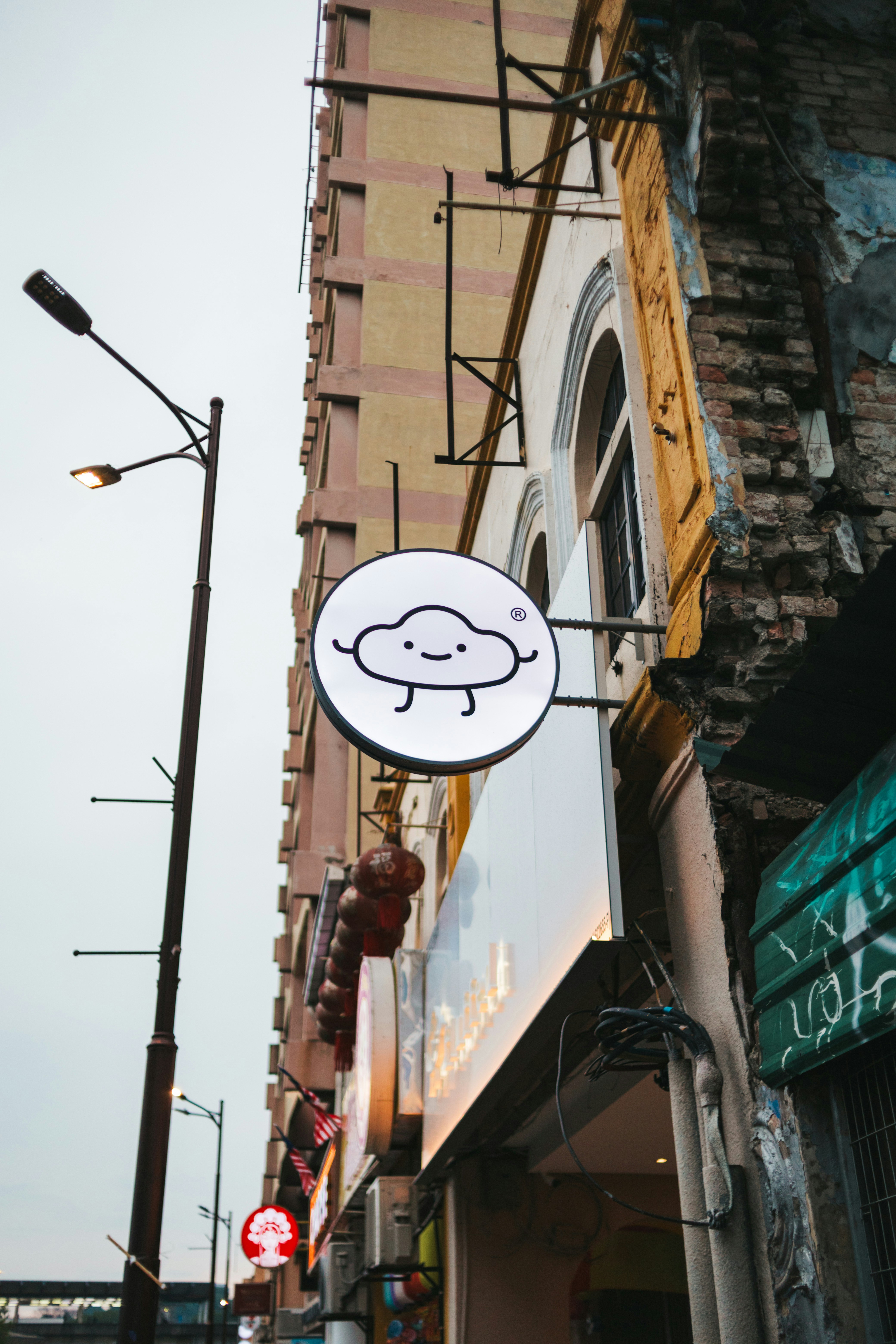 A playful cloud logo hangs prominently outside a building, contrasting with the weathered brickwork and urban surroundings.