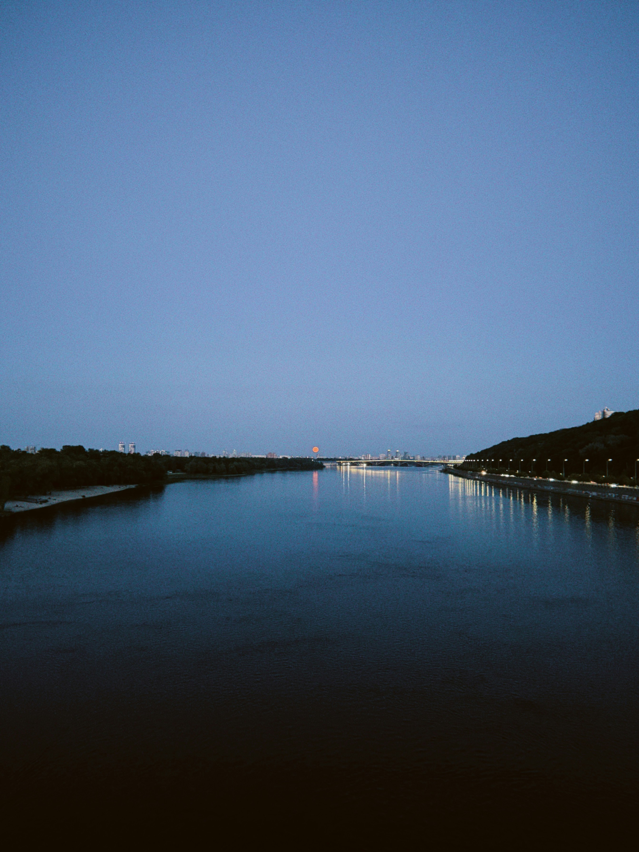 Calm water reflects a clear blue sky at dusk.