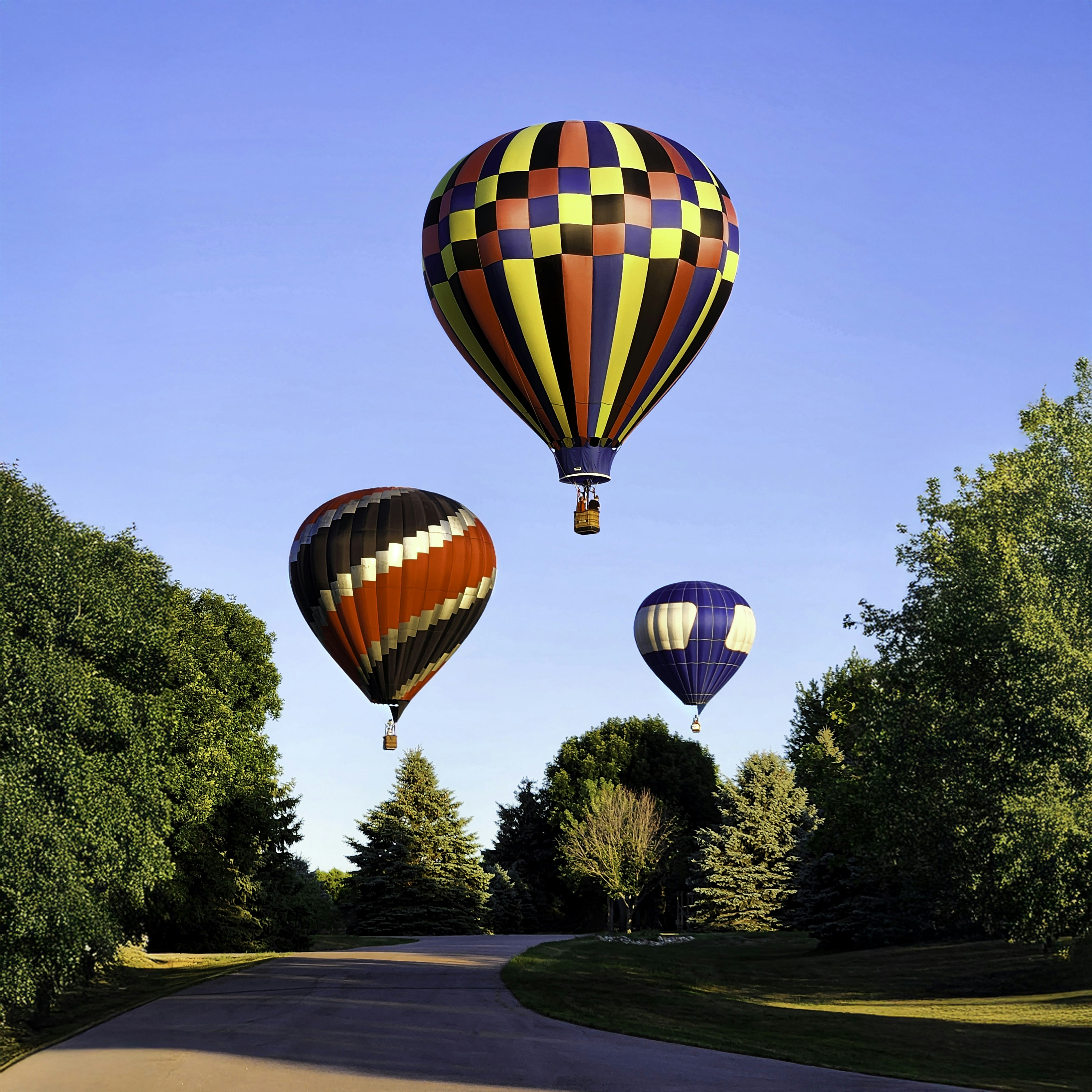 Three colorful hot air balloons ascend into a clear blue sky.