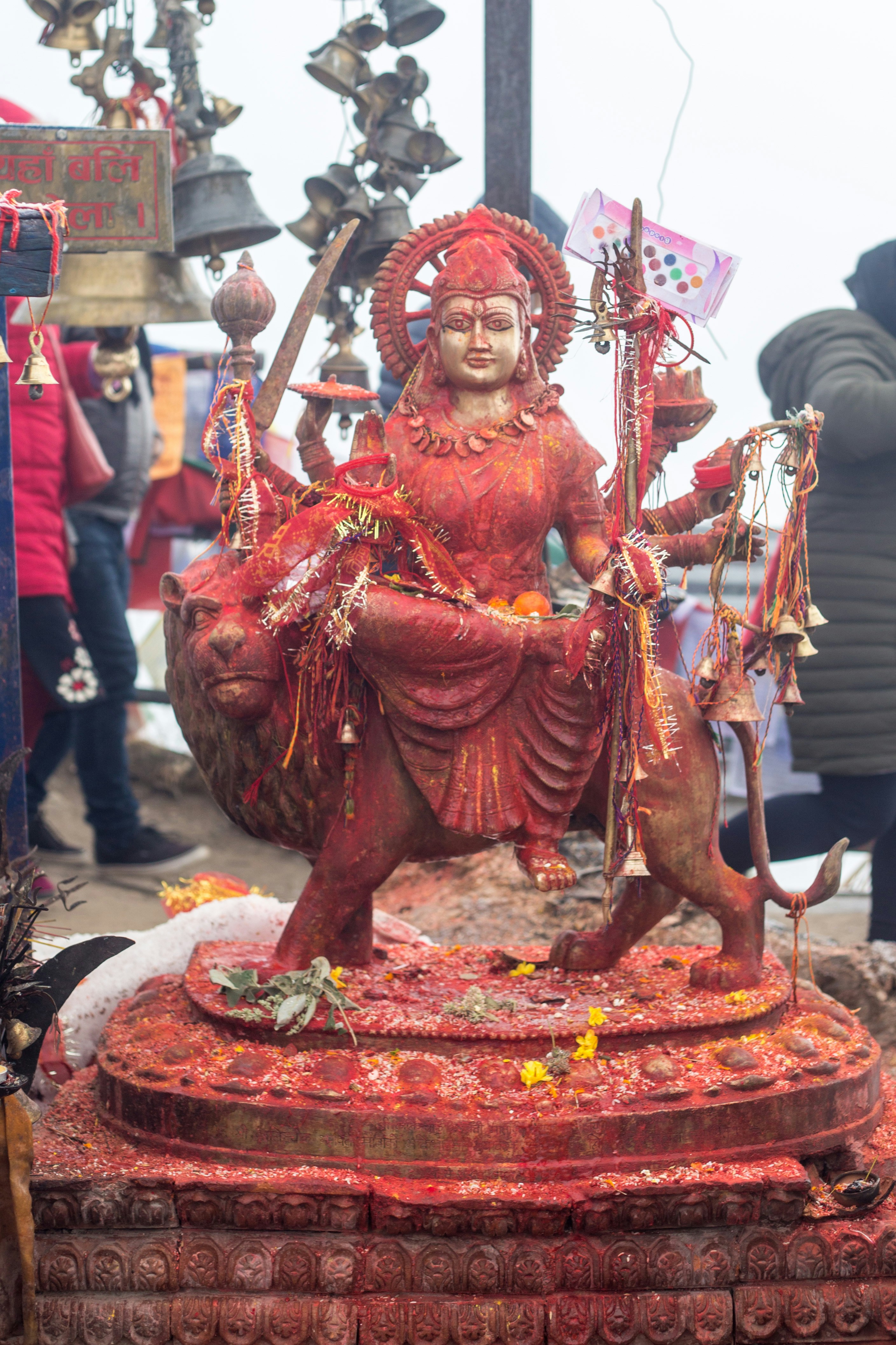 Crimson Goddess on a Prancing Lion: A Shrine Statue Amid Bells and Offerings