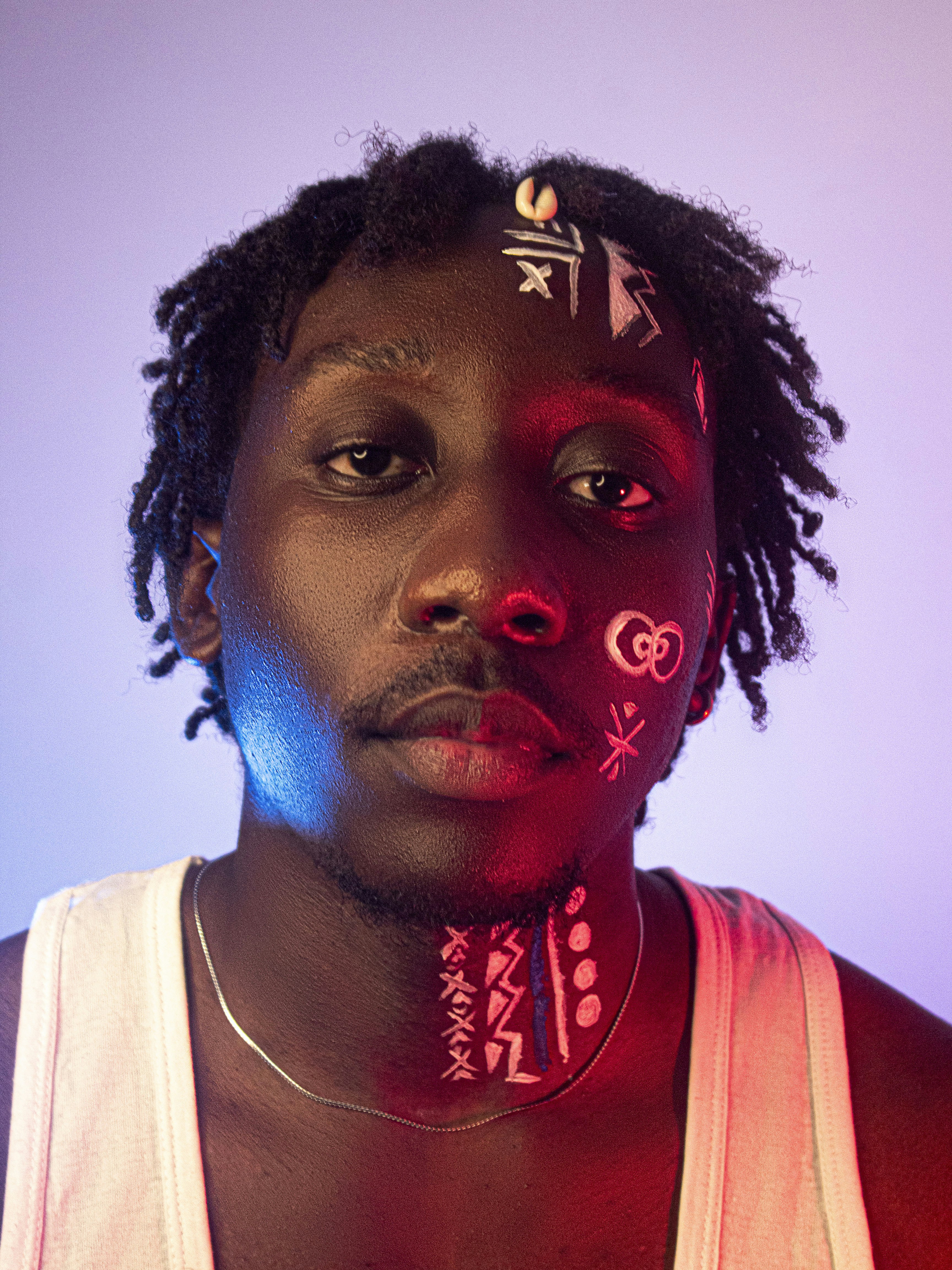 Portrait featuring an individual adorned with intricate facial markings against a softly illuminated backdrop.