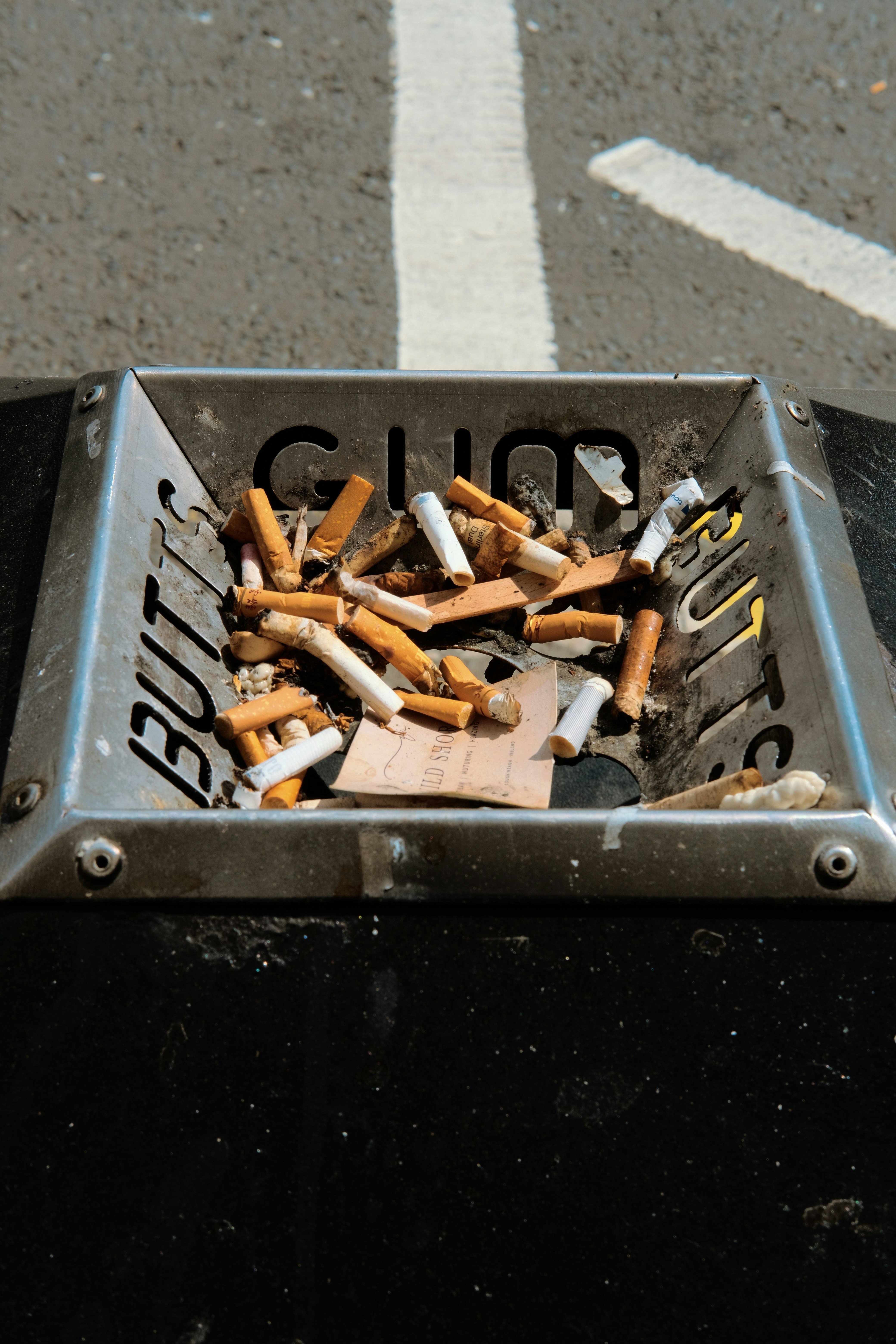 Ashtray filled with discarded cigarette butts and a crumpled note resting on top. A stark reminder of urban life and its waste.