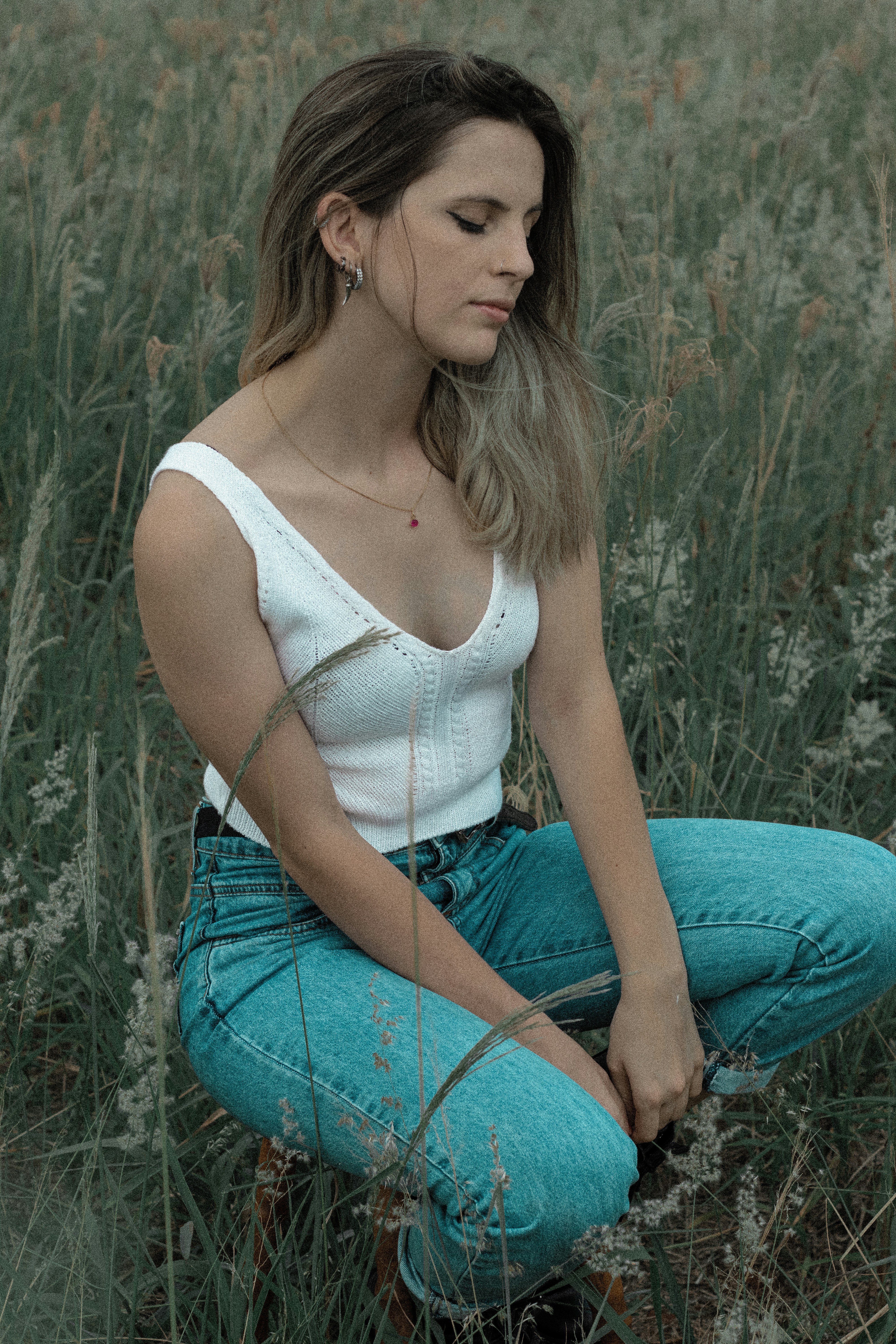 Woman in white top and blue jeans sitting in grass