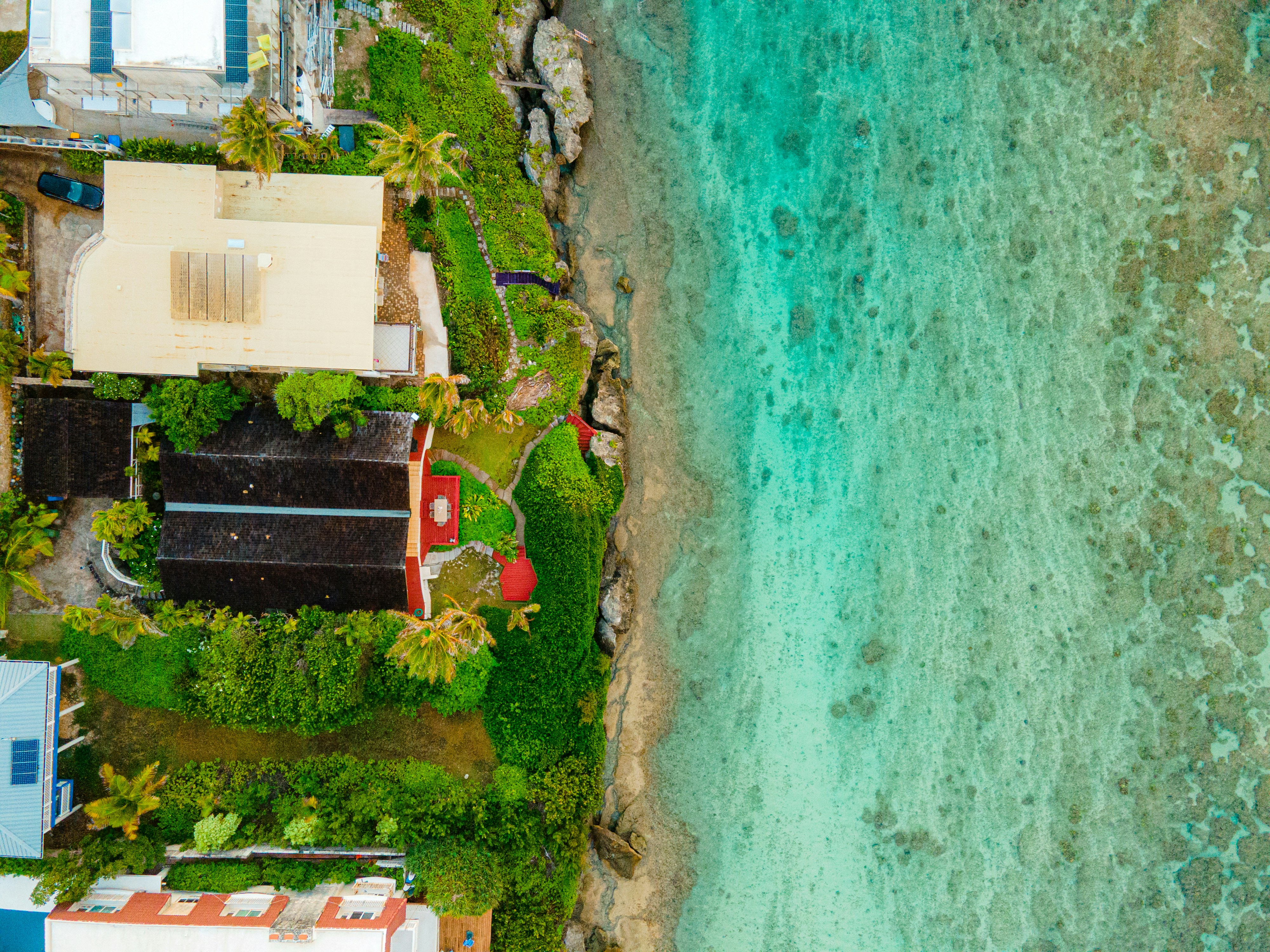 Aerial view of a coastal property surrounded by lush greenery and turquoise waters, showcasing the harmony between nature and architecture.