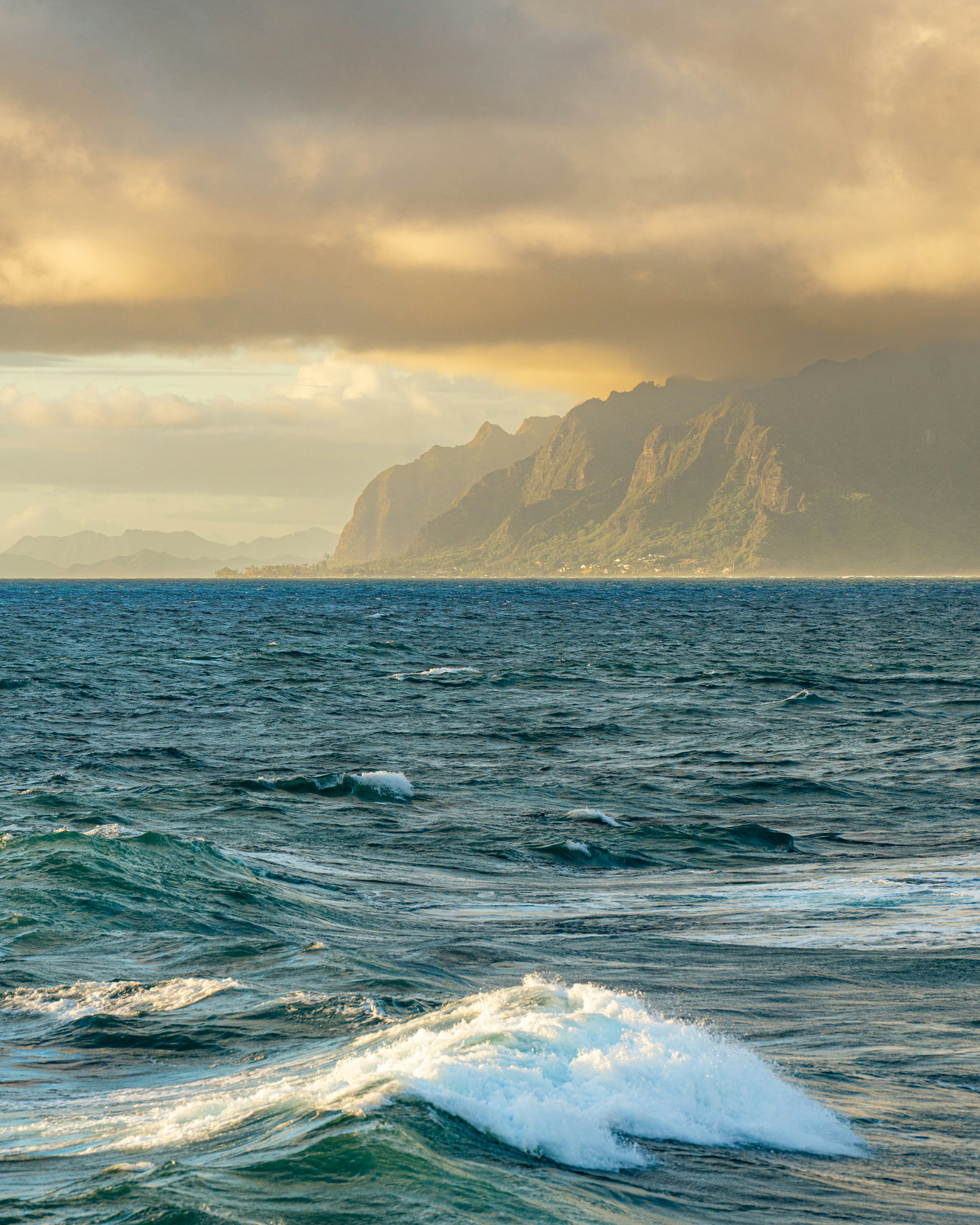 Waves gently lap against the shore under a dramatic sky, with rugged mountains rising in the background. A serene moment captured in nature's embrace.