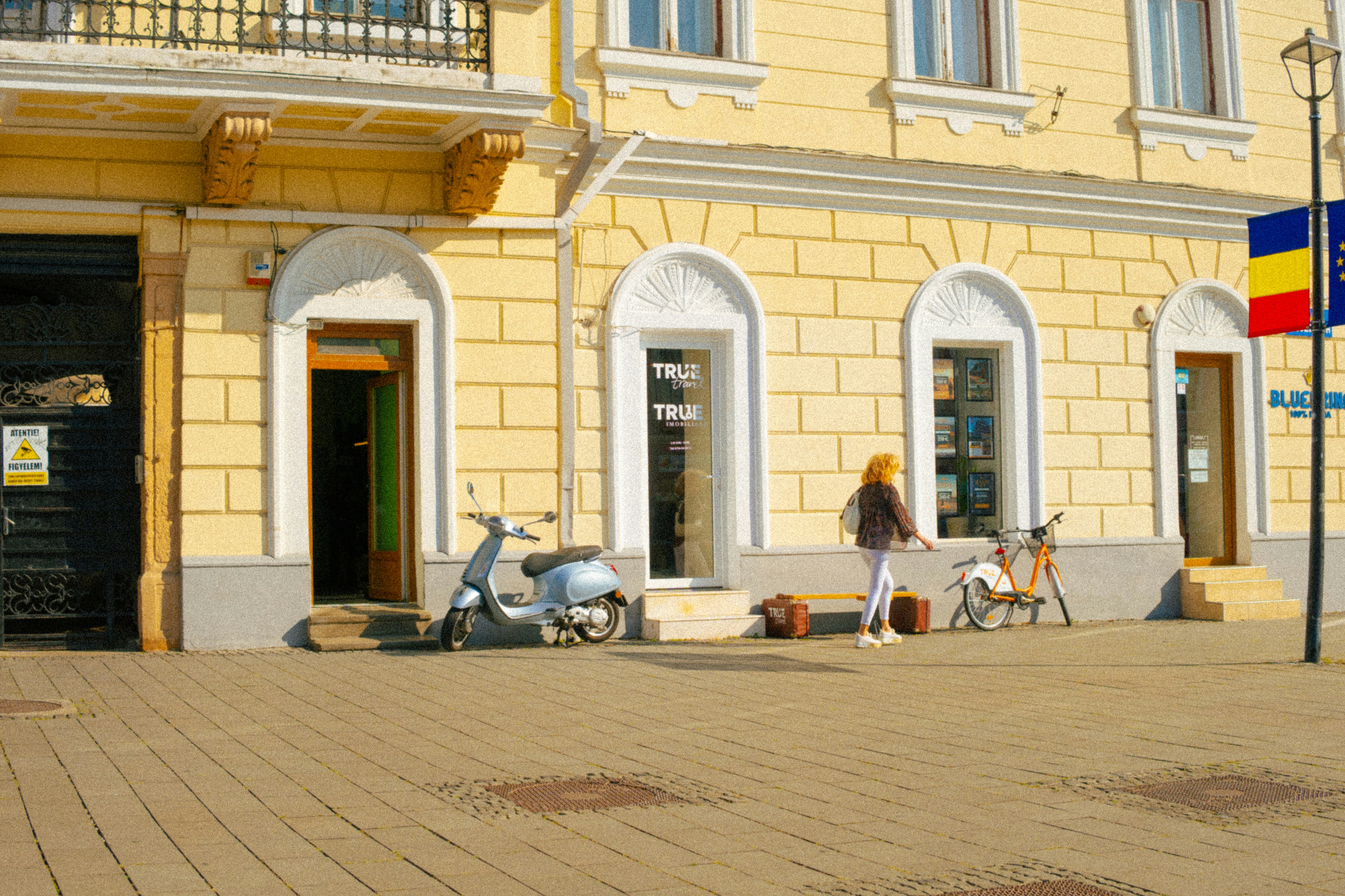 A candid street moment in Cluj, showcasing the city’s unique character and timeless atmosphere. | Yellow building facade with arched windows and parked scooters.
