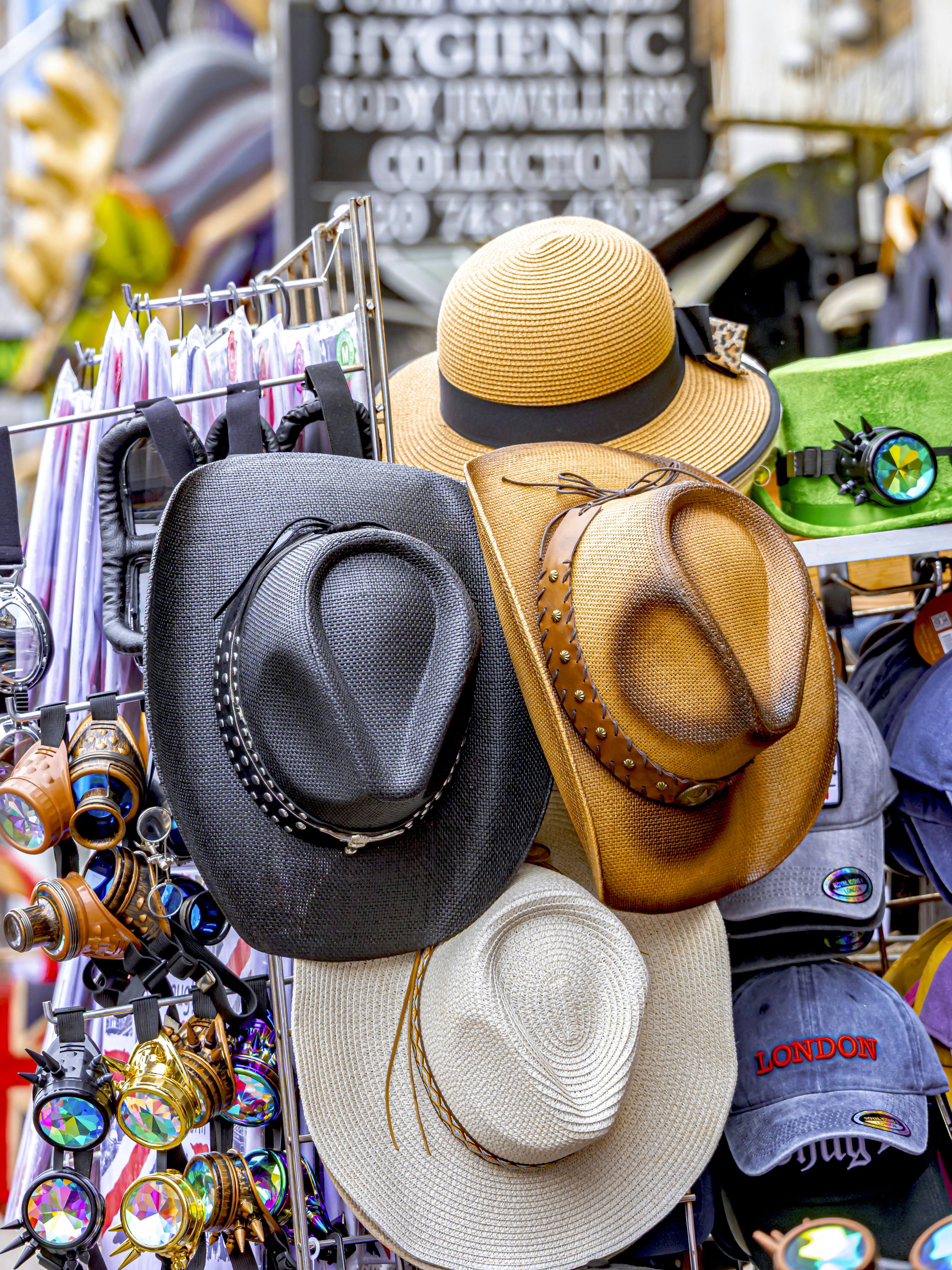 Variety of hats including cowboy and straw styles arranged on a bustling market stall, showcasing urban fashion trends.