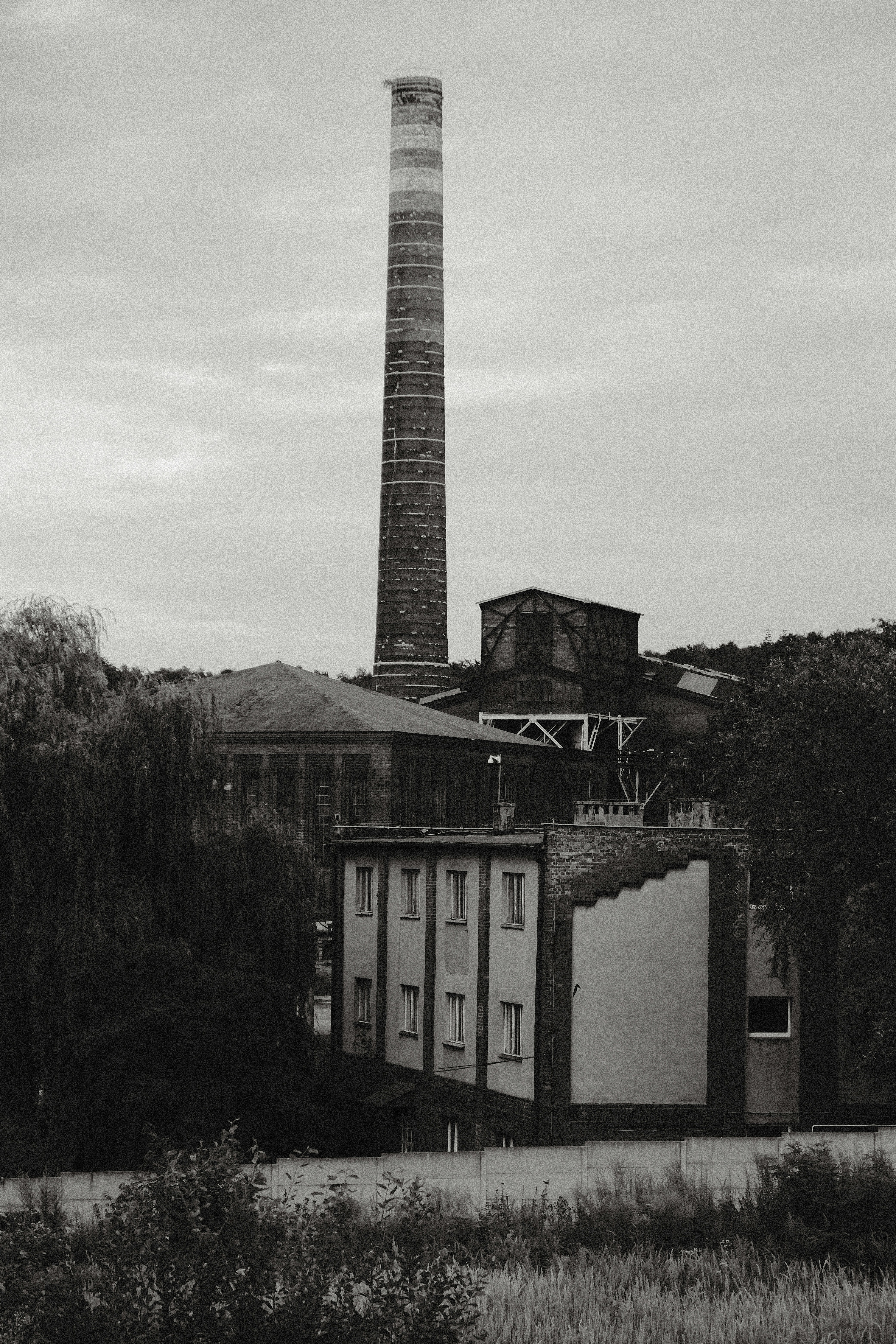 Industrial building with tall smokestack under cloudy sky