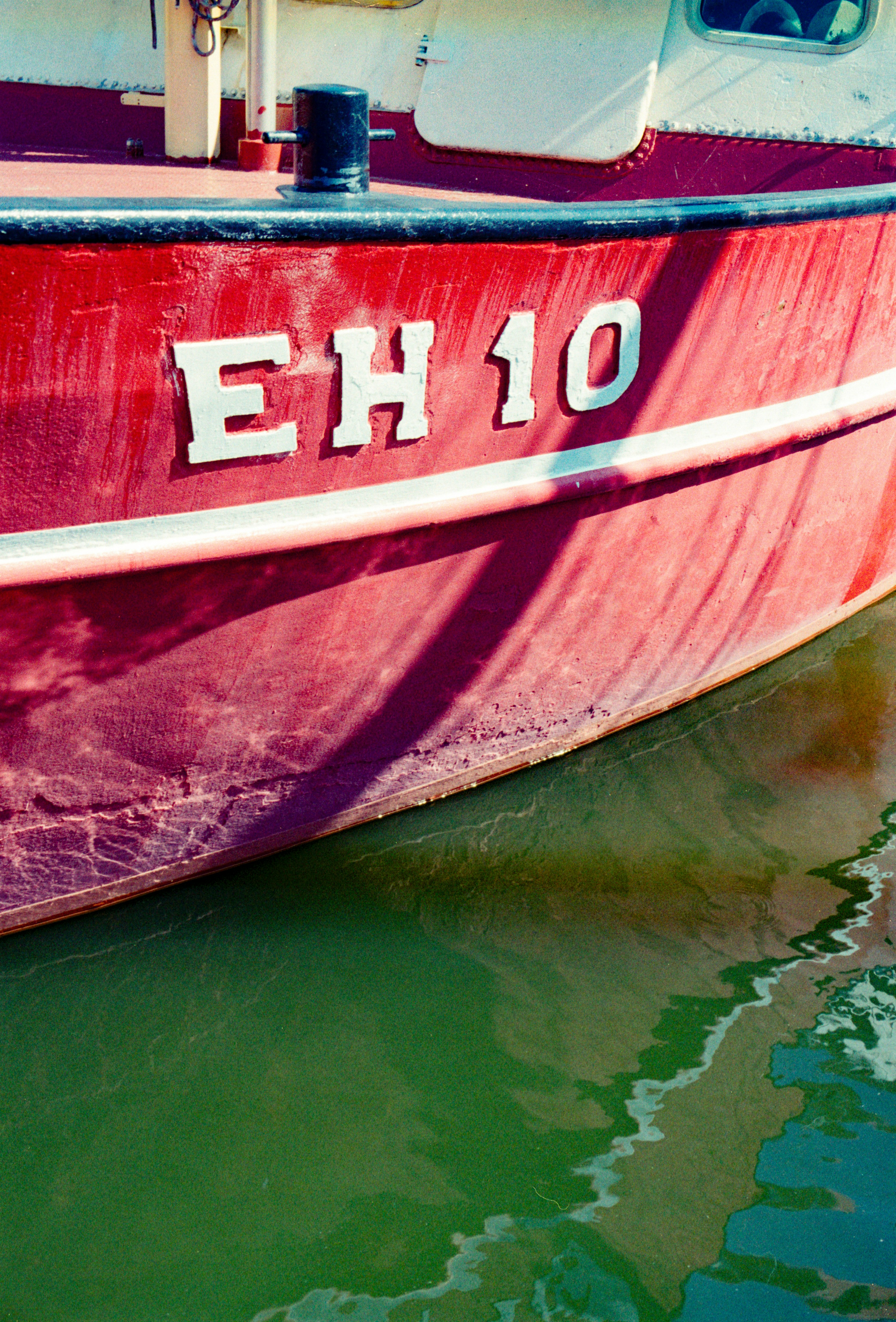 Close-up of a weathered fishing boat's hull displaying the registration number 'EH 10' against a backdrop of shimmering green water.