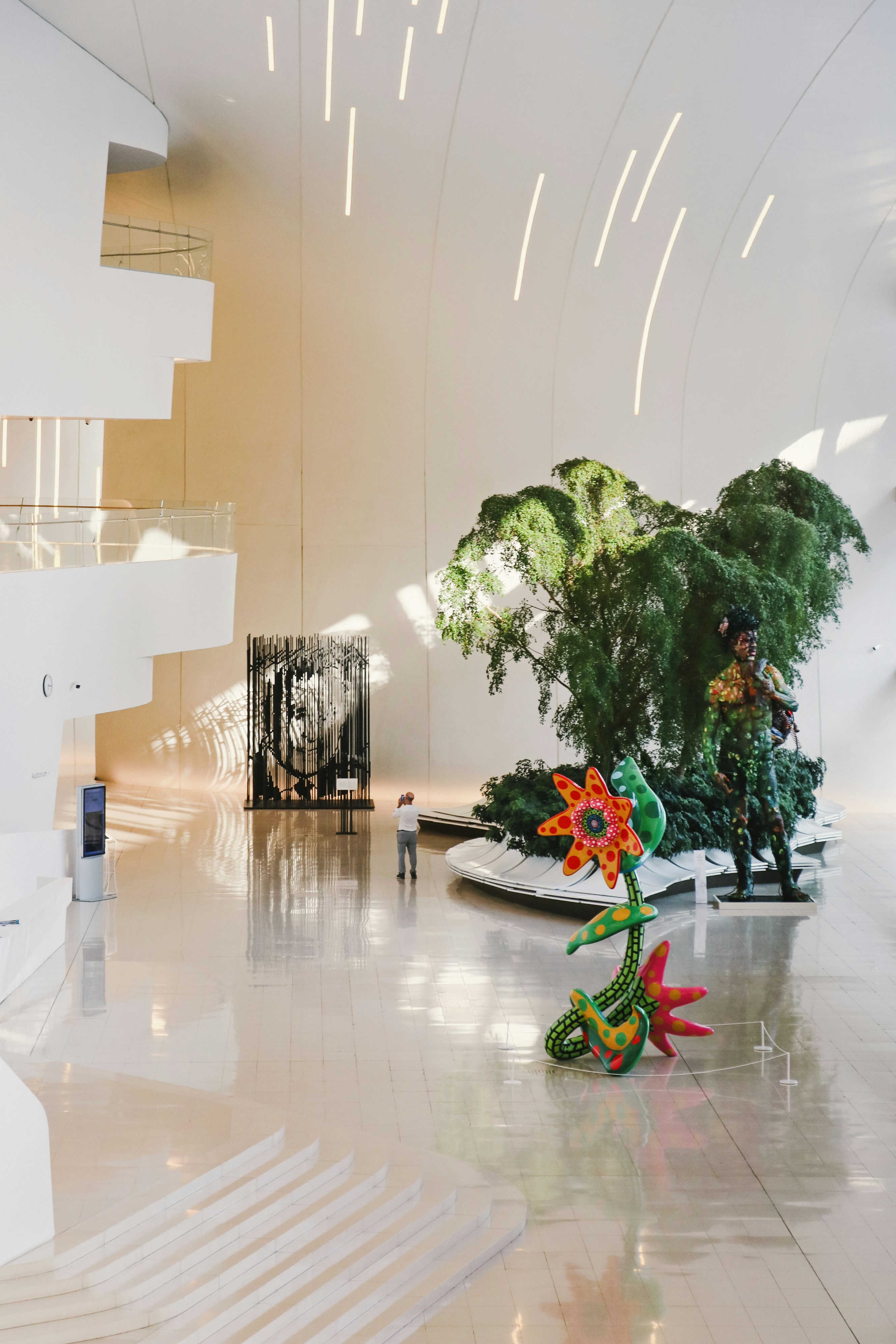 A vibrant, whimsical sculpture entwined with flora contrasts against a sleek architectural interior, highlighting the interplay of art and nature.