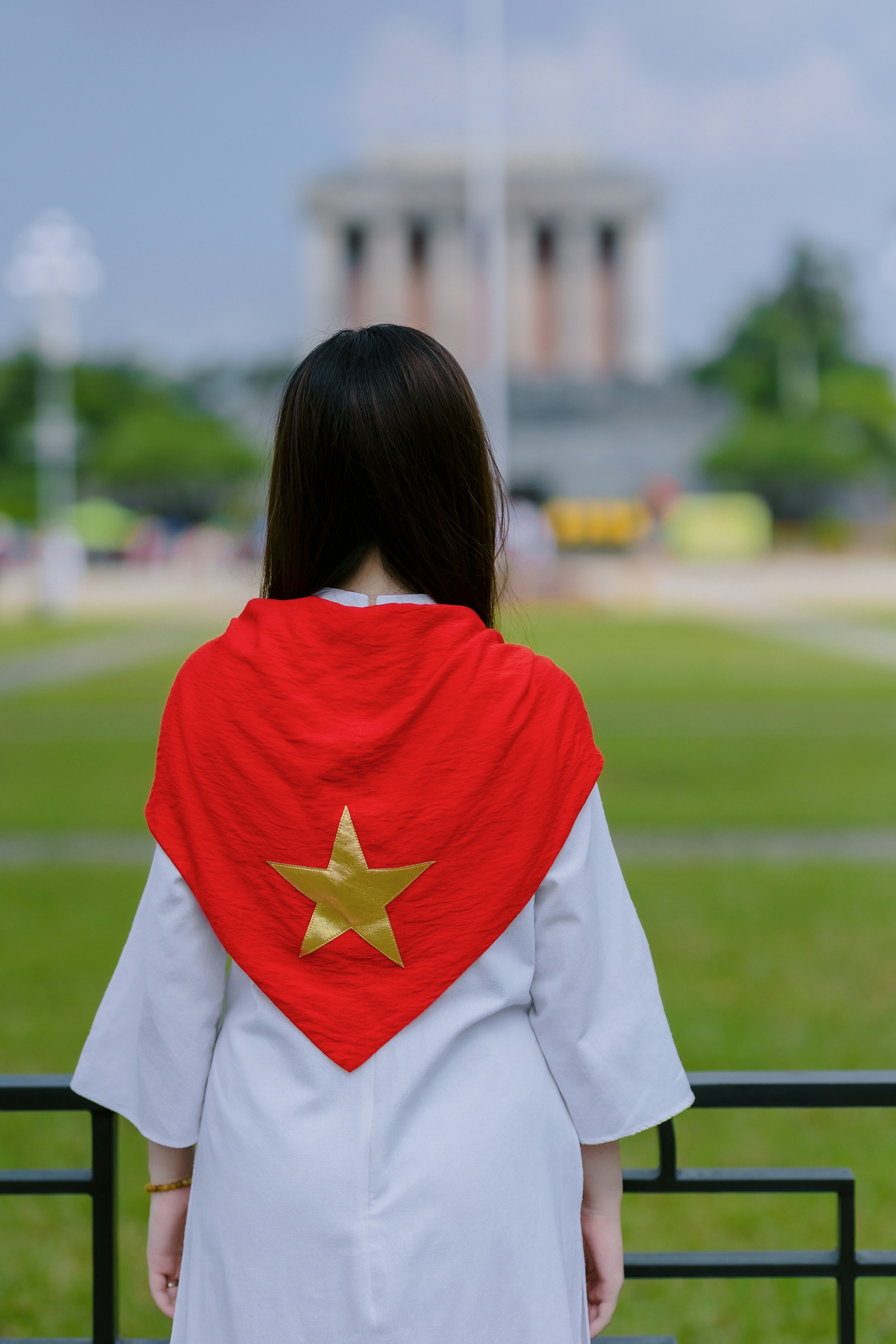 Individual in traditional attire with a red cape featuring a golden star, gazing towards a historic monument in the background.