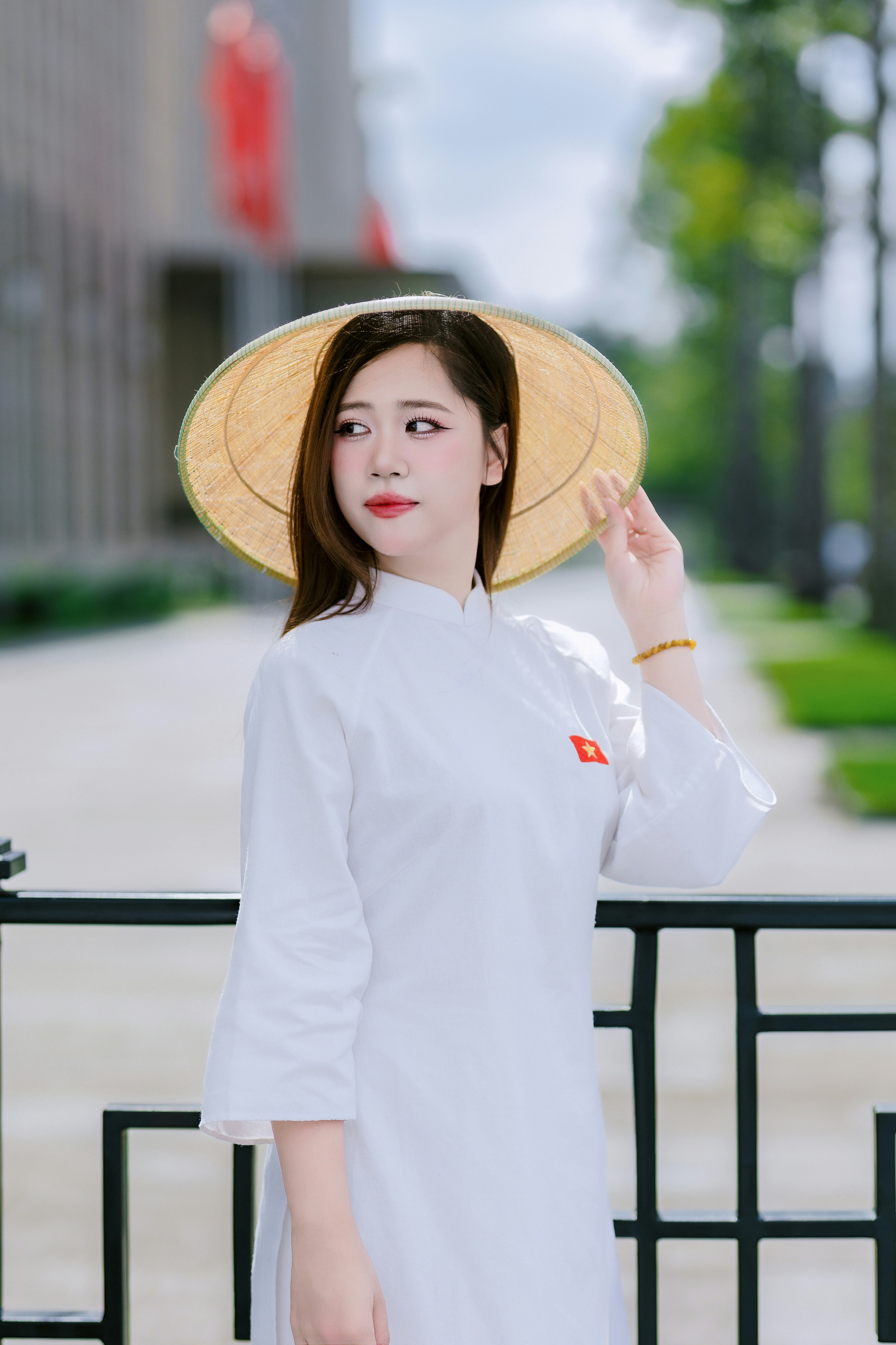 Young woman in traditional attire and straw hat poses gracefully against a blurred urban backdrop. Her expression reflects serenity and cultural pride.